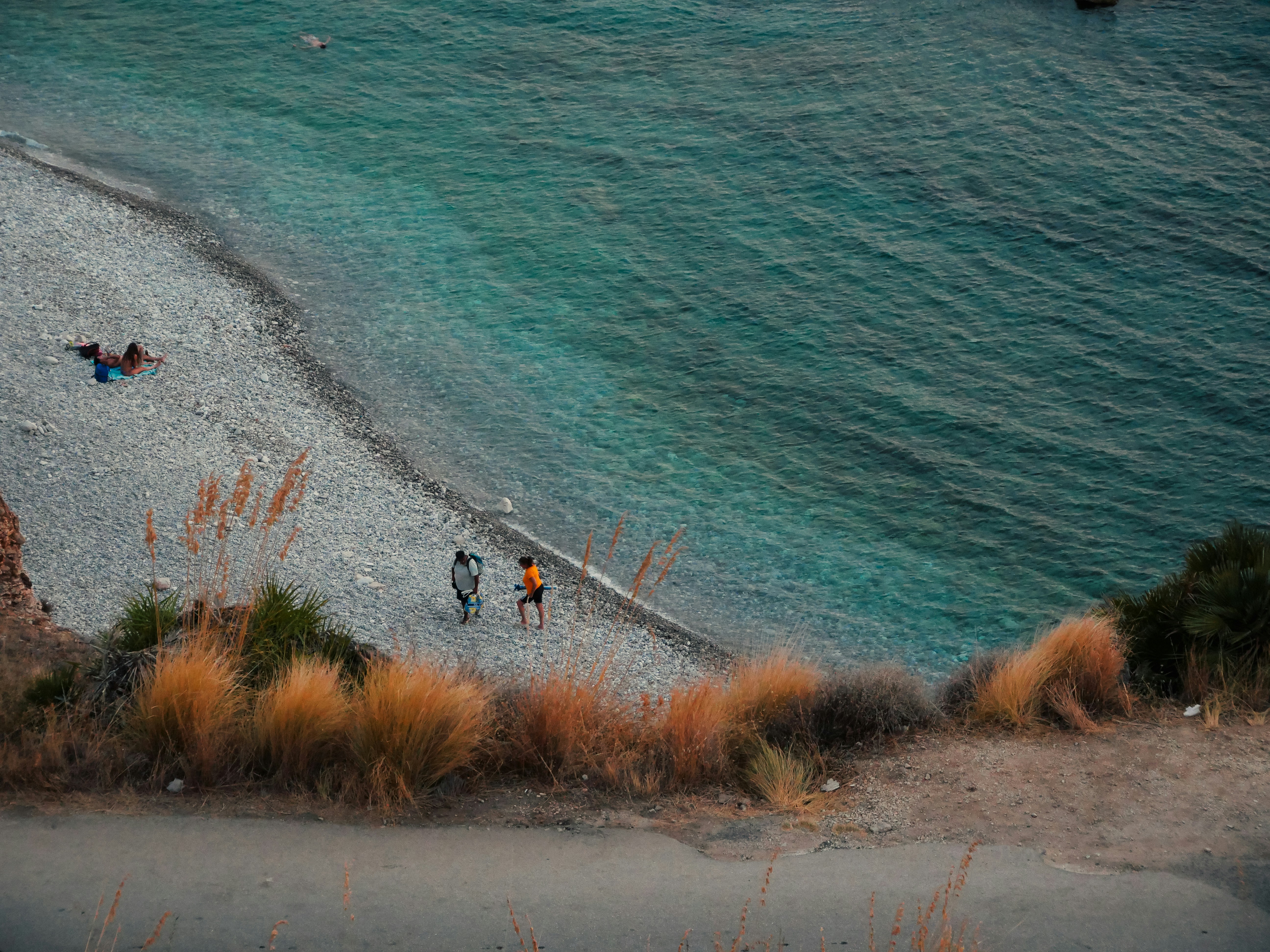 Coastal hikers amid dune grasses overlooking a pebble beach