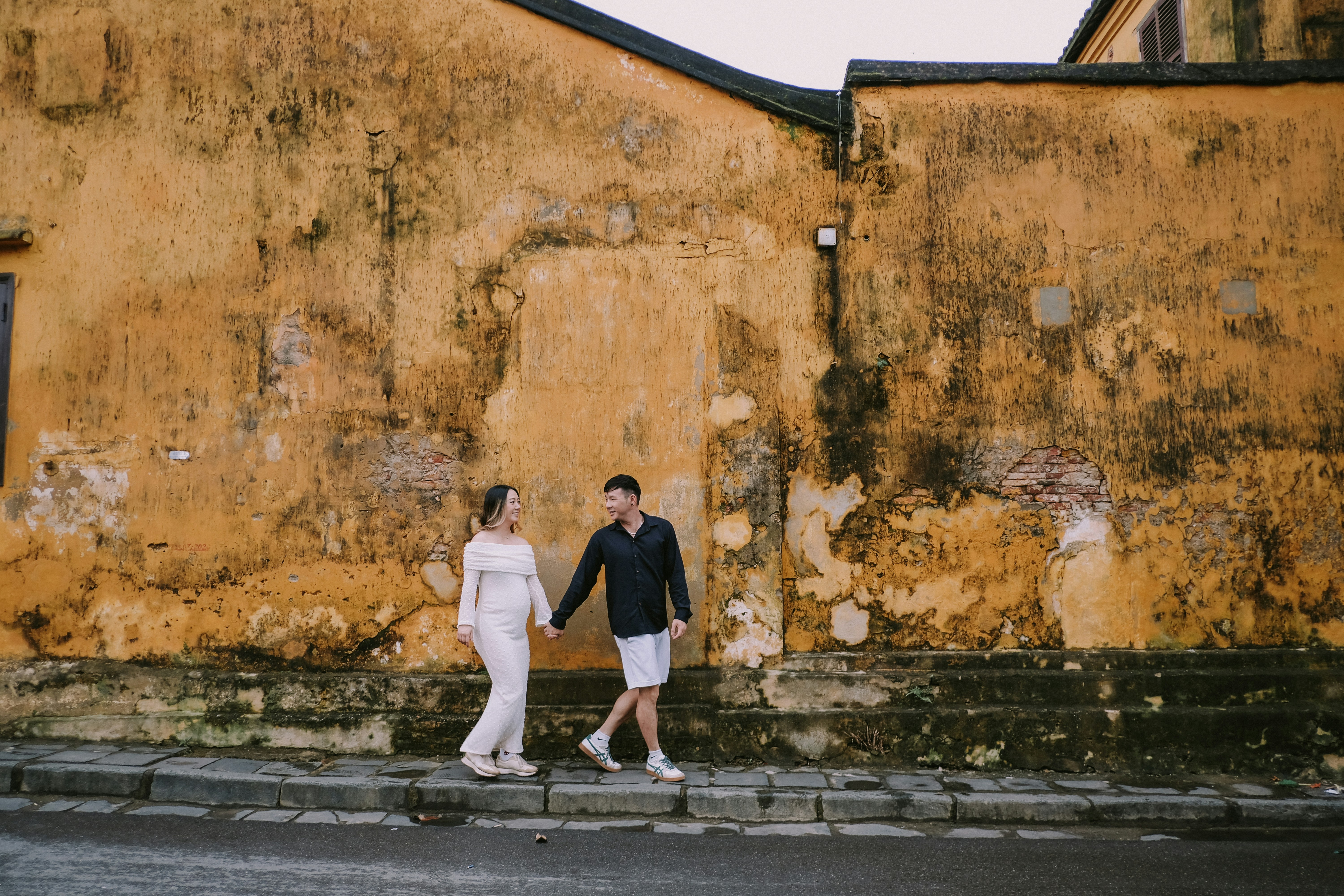 Yellow Wall Stroll: A Couple in Quiet Motion Along a Heritage Facade