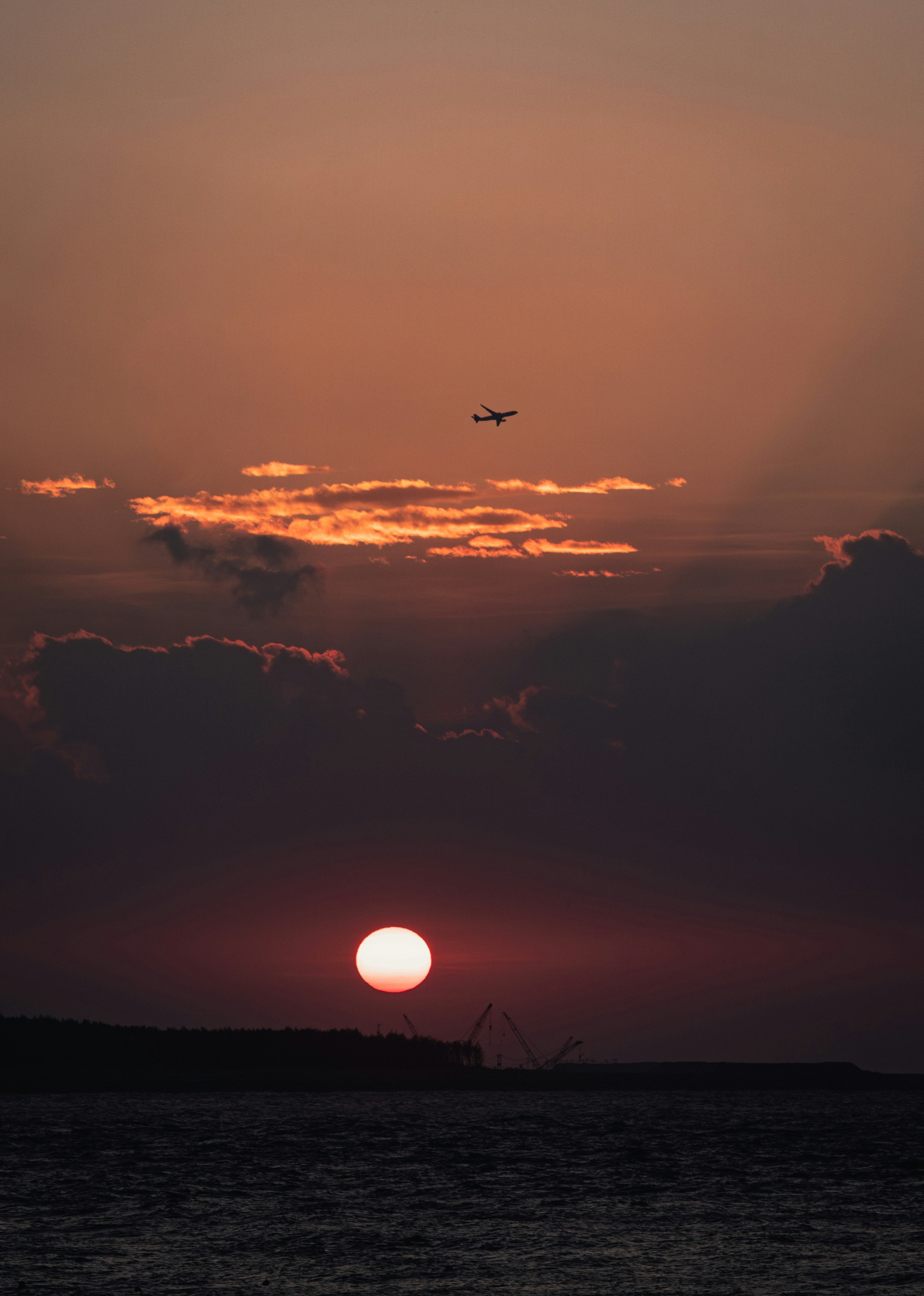 Sun Dip Over Quiet Horizon: A Distant Plane Silhouette Against a Crimson Sky