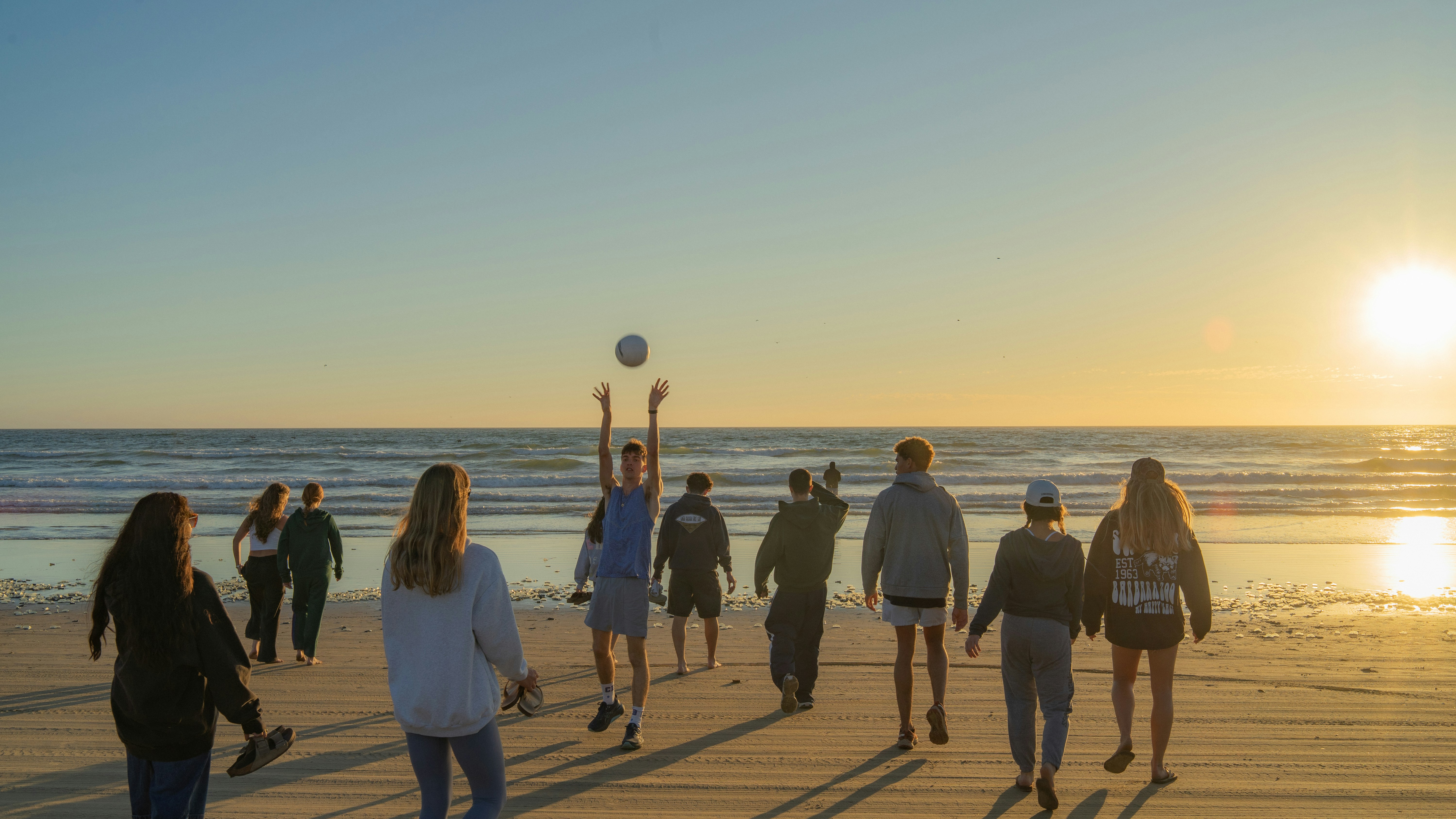 Group on the Shimmering Beach: Sunset Ball in Flight