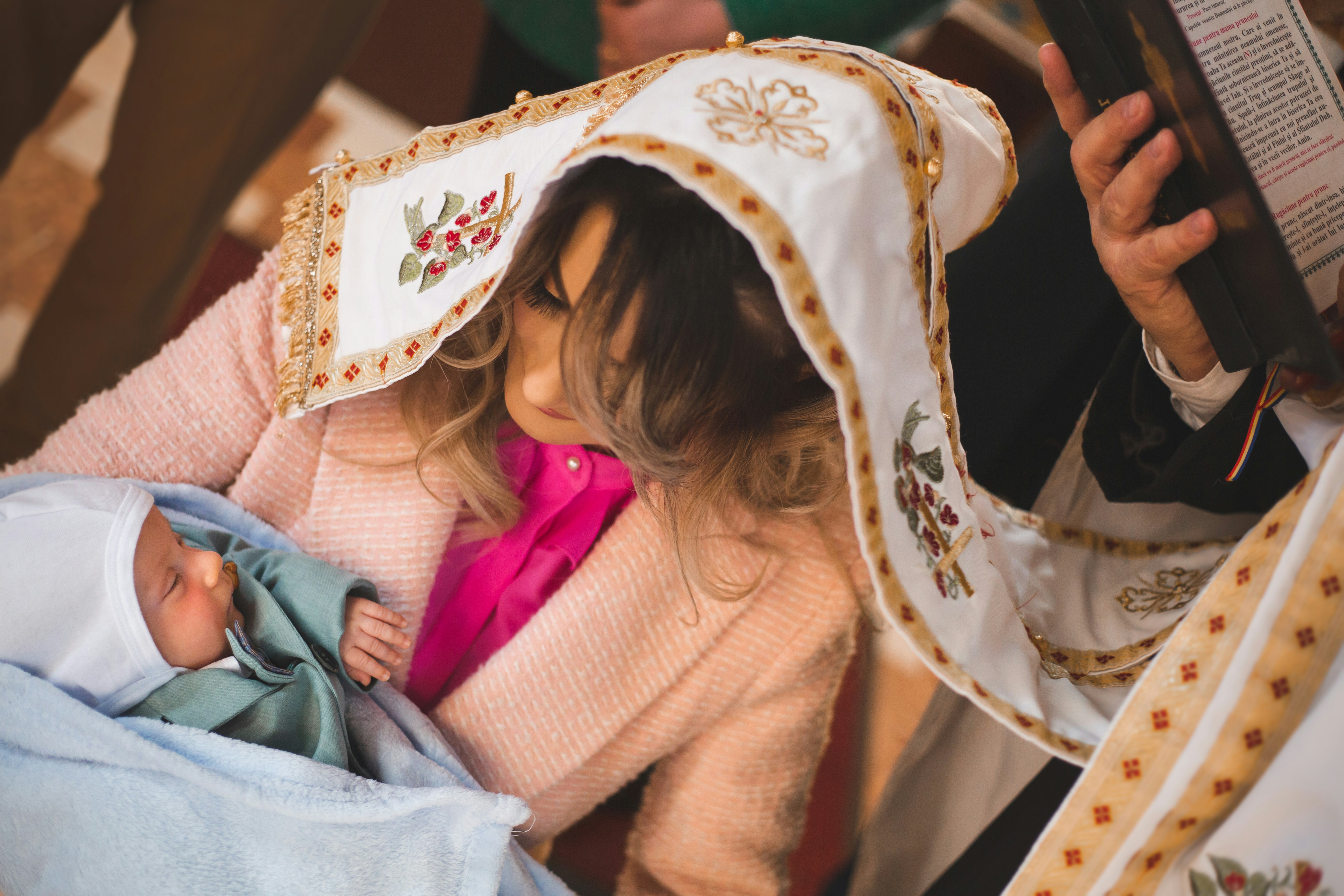 Mother in front of the priest, holding her young baby boy, and looking at him.