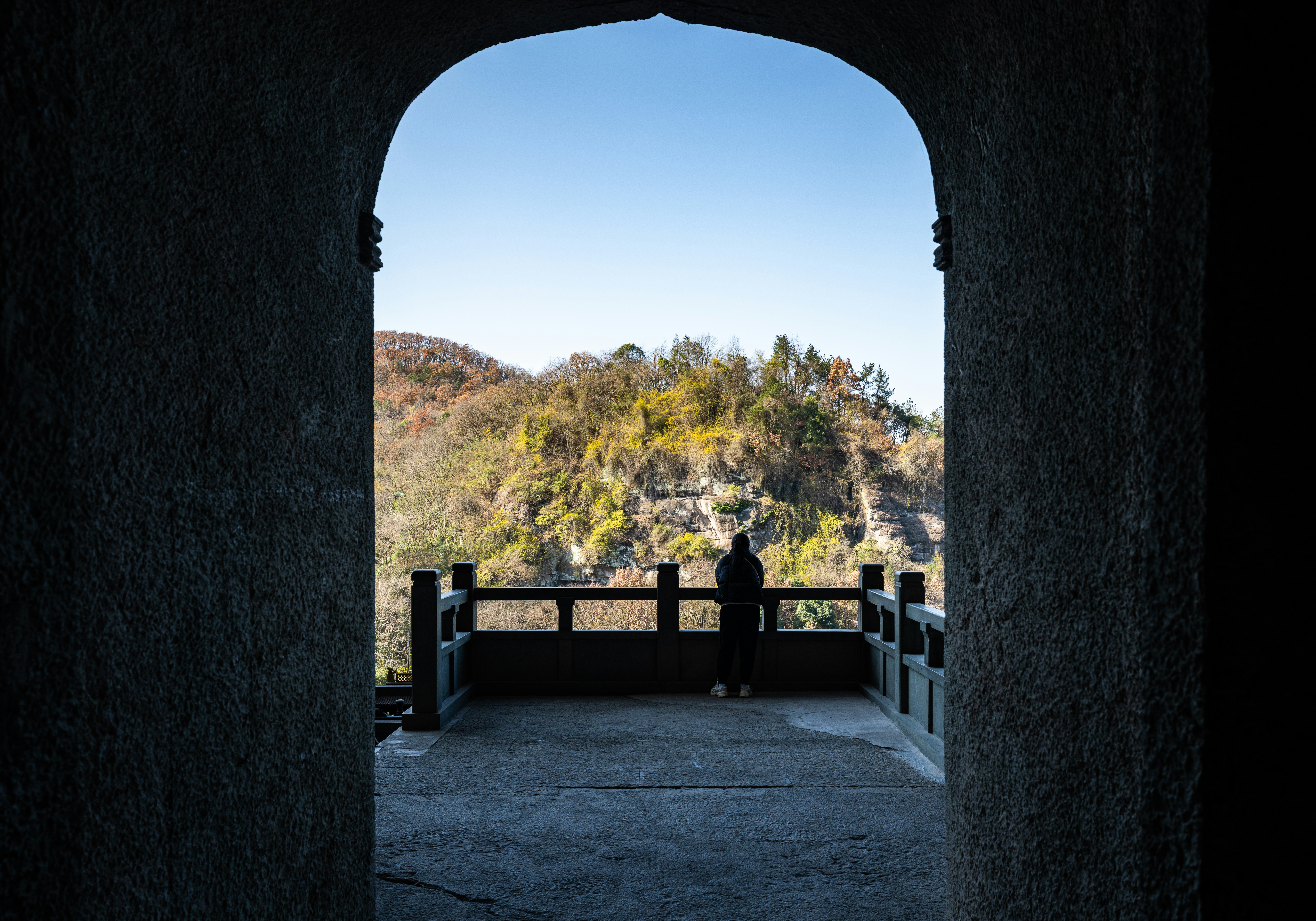 Hidden Balcony View: Figure Framed by Archway to a Misty Cliffscape