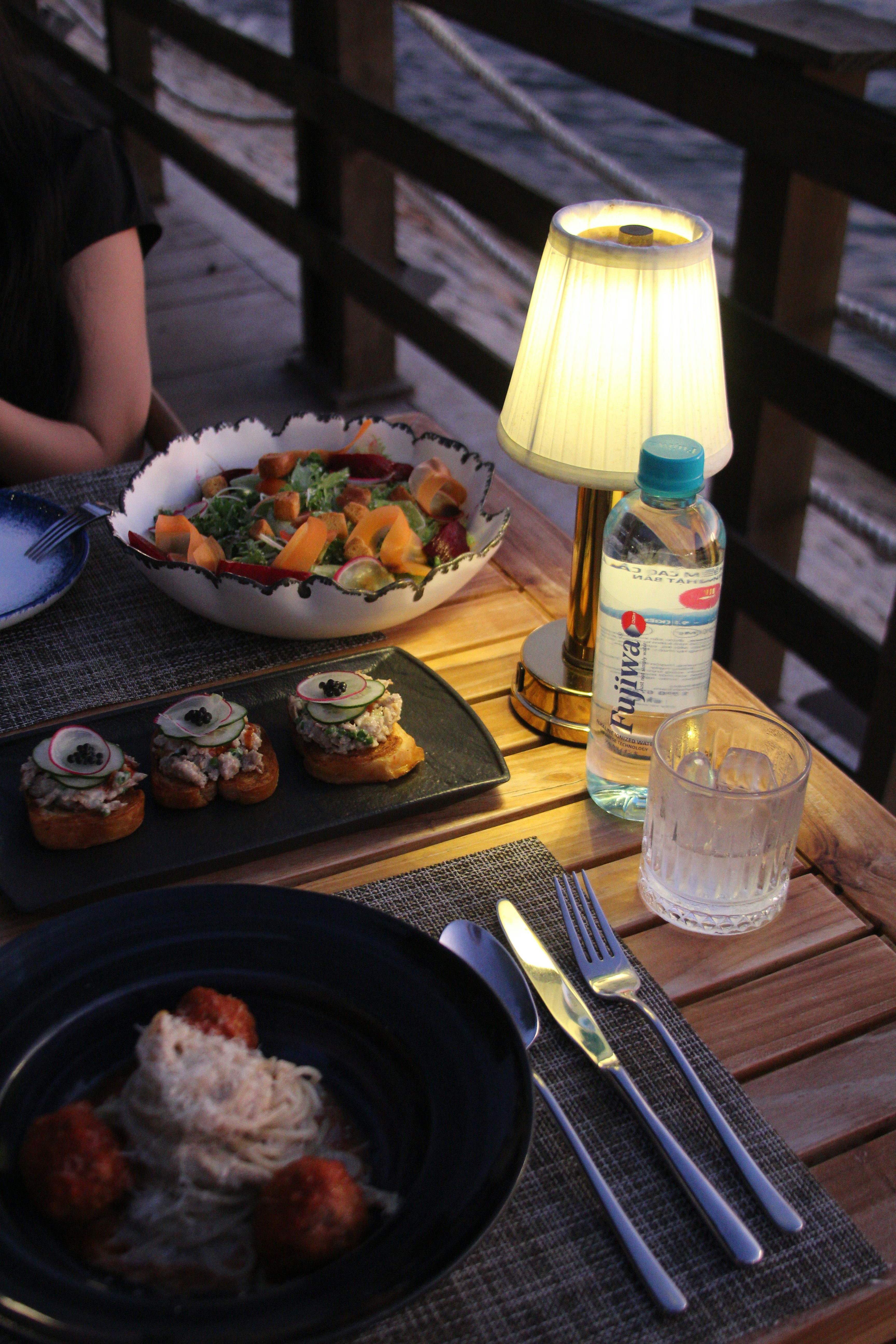 Dim candlelight, vibrant plates: a seaside dinner on wood and glow