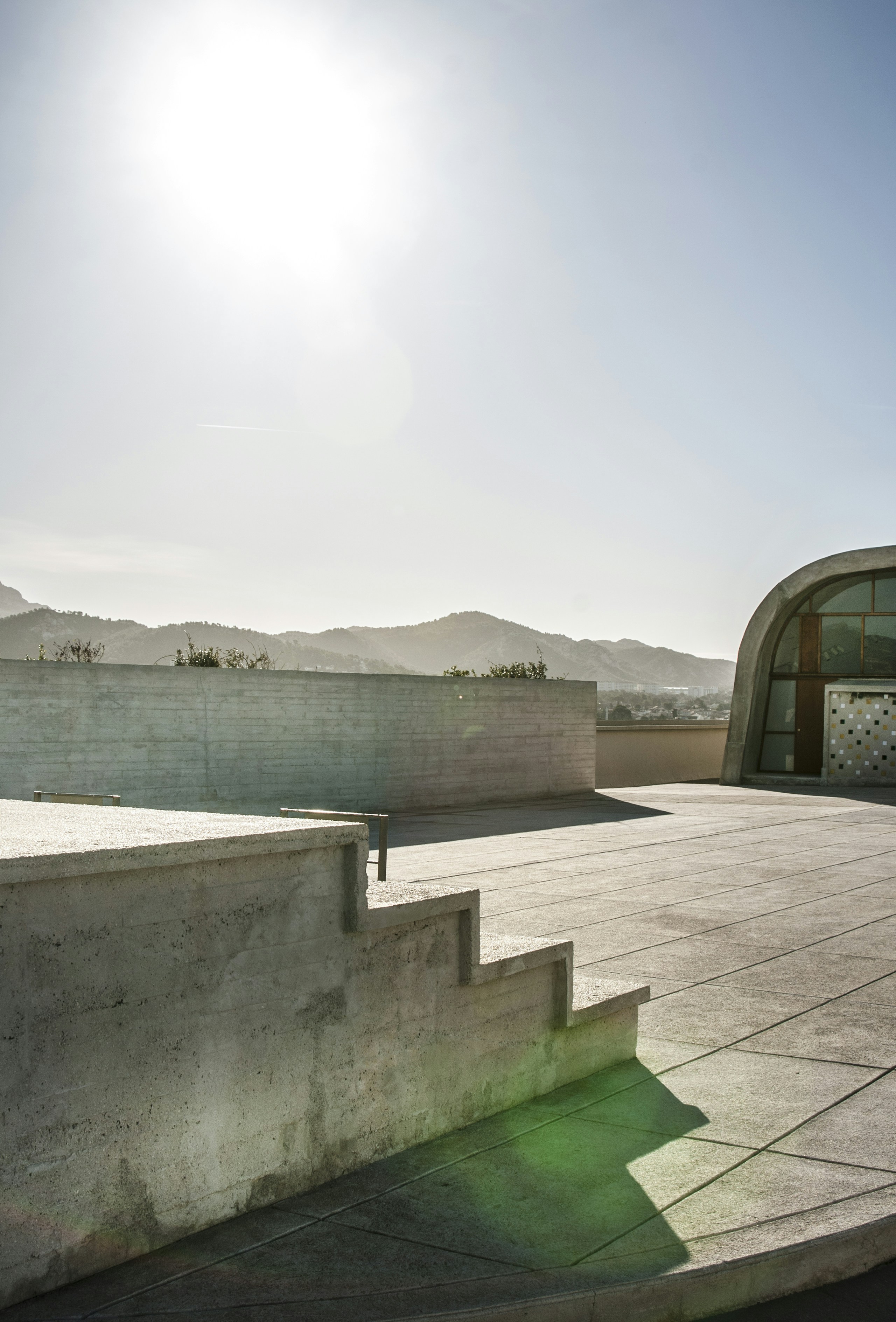 Sunlit rooftop steps toward a curved glass pavilion
