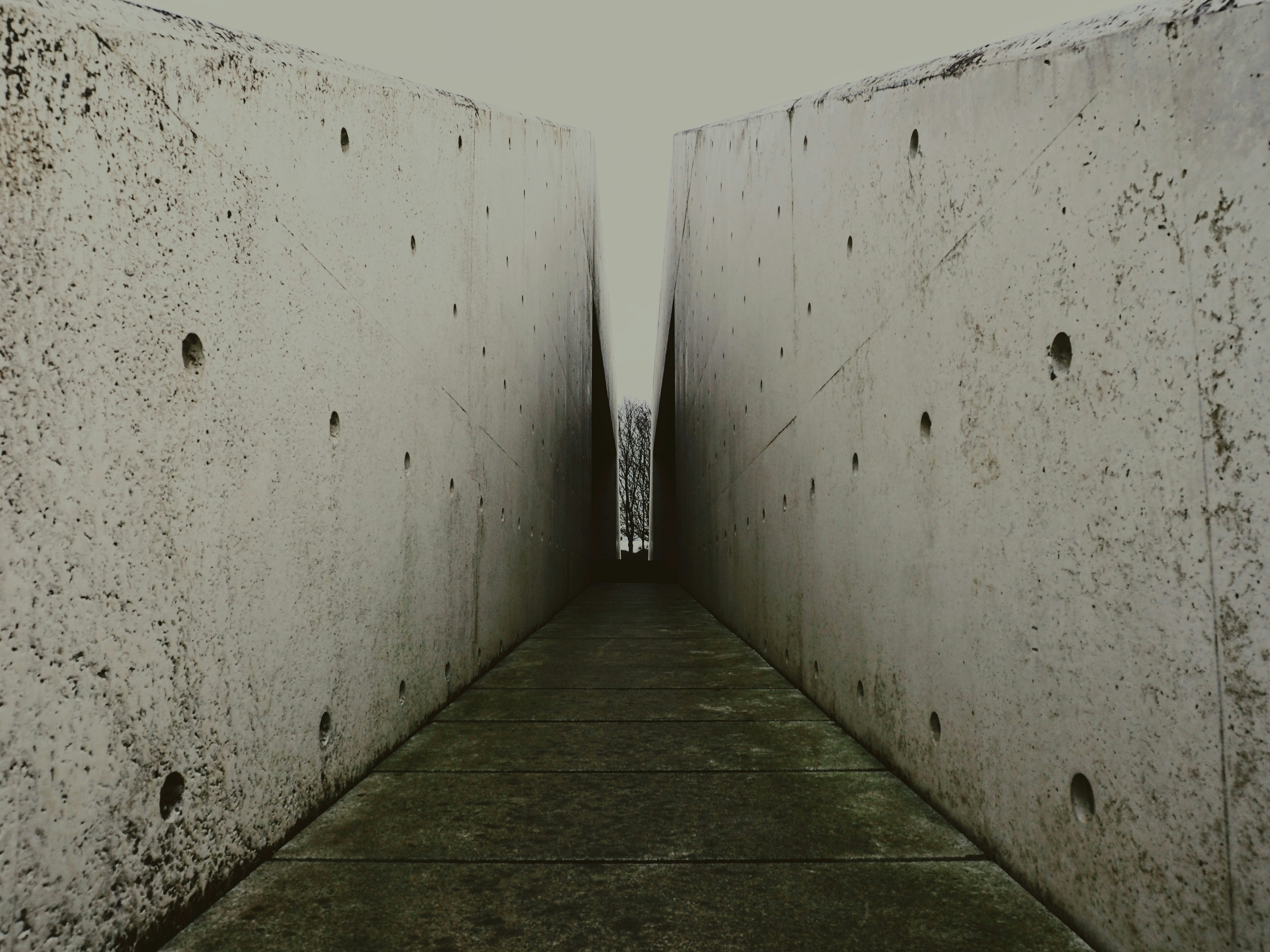 A narrow concrete passage within the Tulach a’ tSolais monument, built to commemorate the 1798 Rebellion in County Wexford, Ireland. Strong symmetry, converging lines, and muted tones create a contemplative space that draws the eye toward light, reinforcing themes of memory, reflection, and history.
