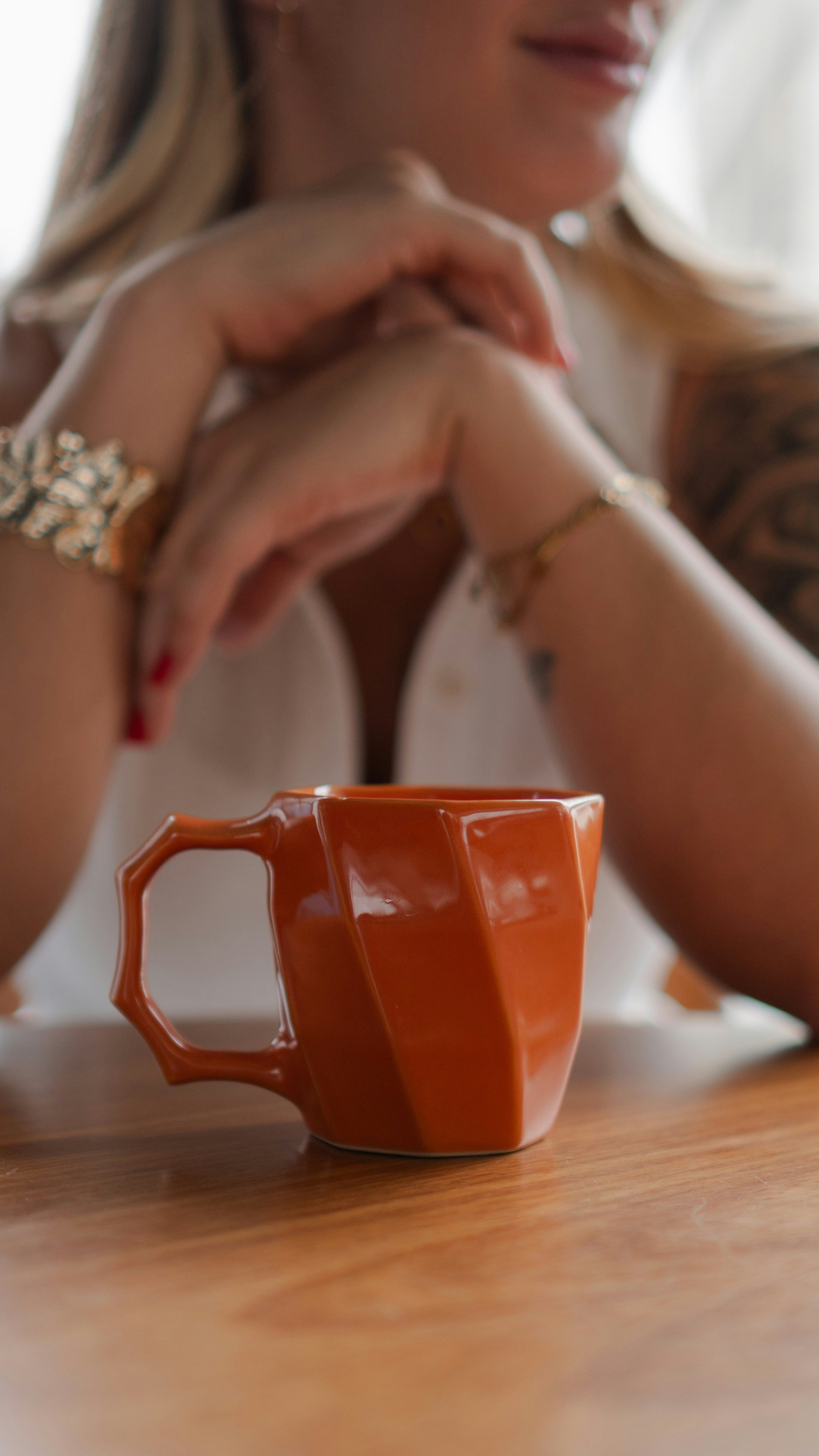 Hands Folded, Orange Mug in Focus: A Quiet Moment Over Coffee