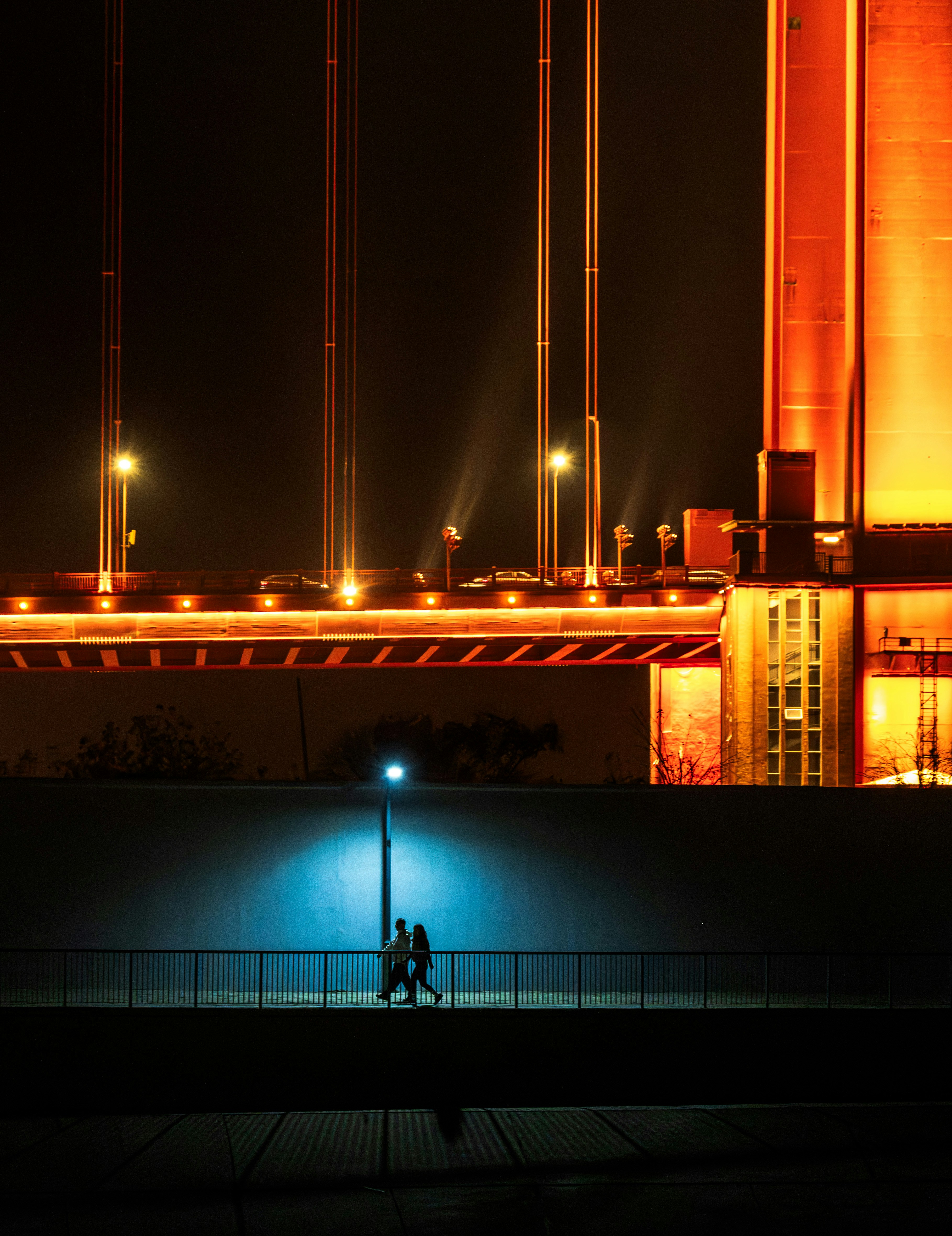 Blue-lit silhouette under a radiant orange bridge tower