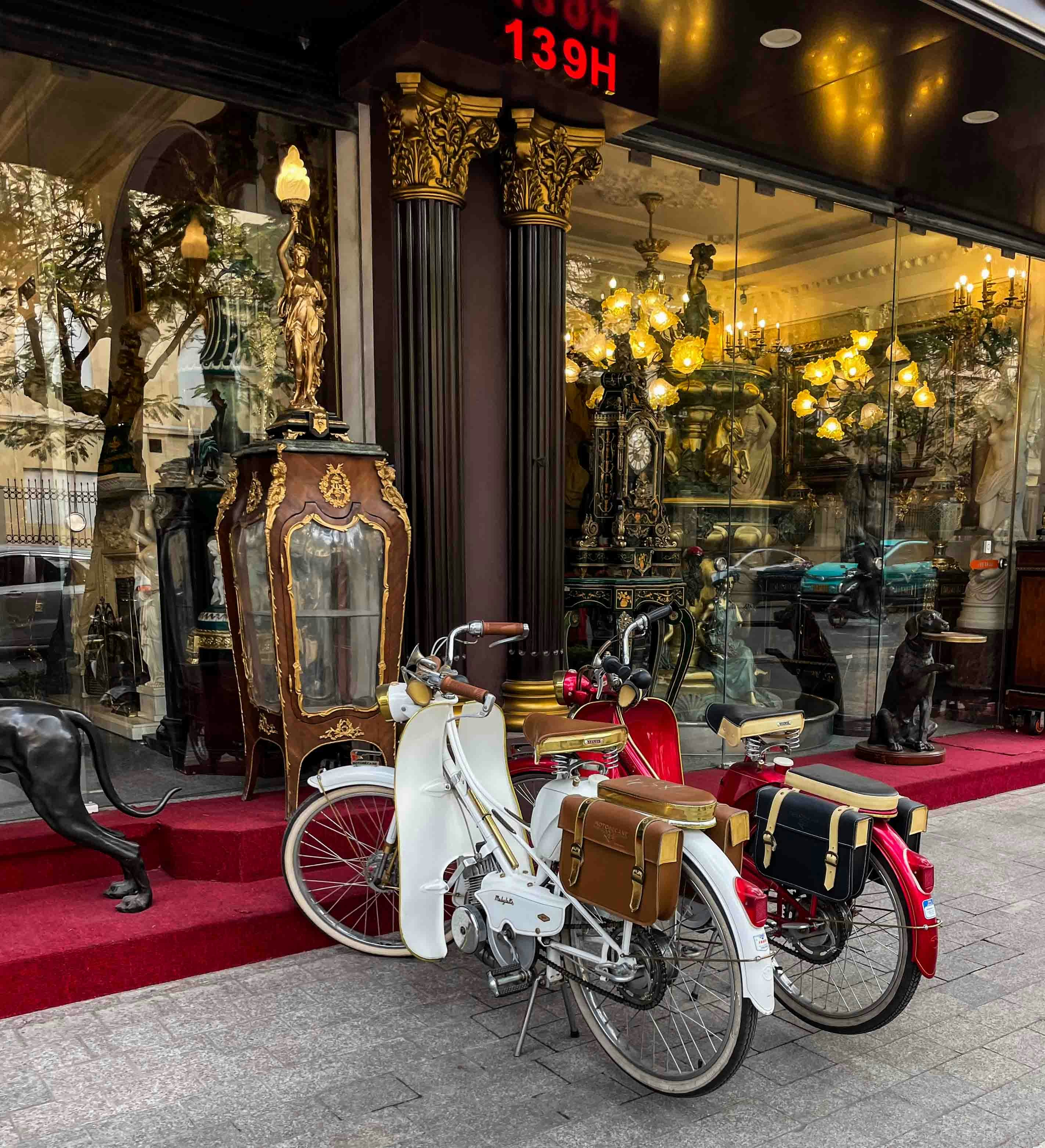 Vintage bicycles by a gilded storefront emerge from a reflective shop window