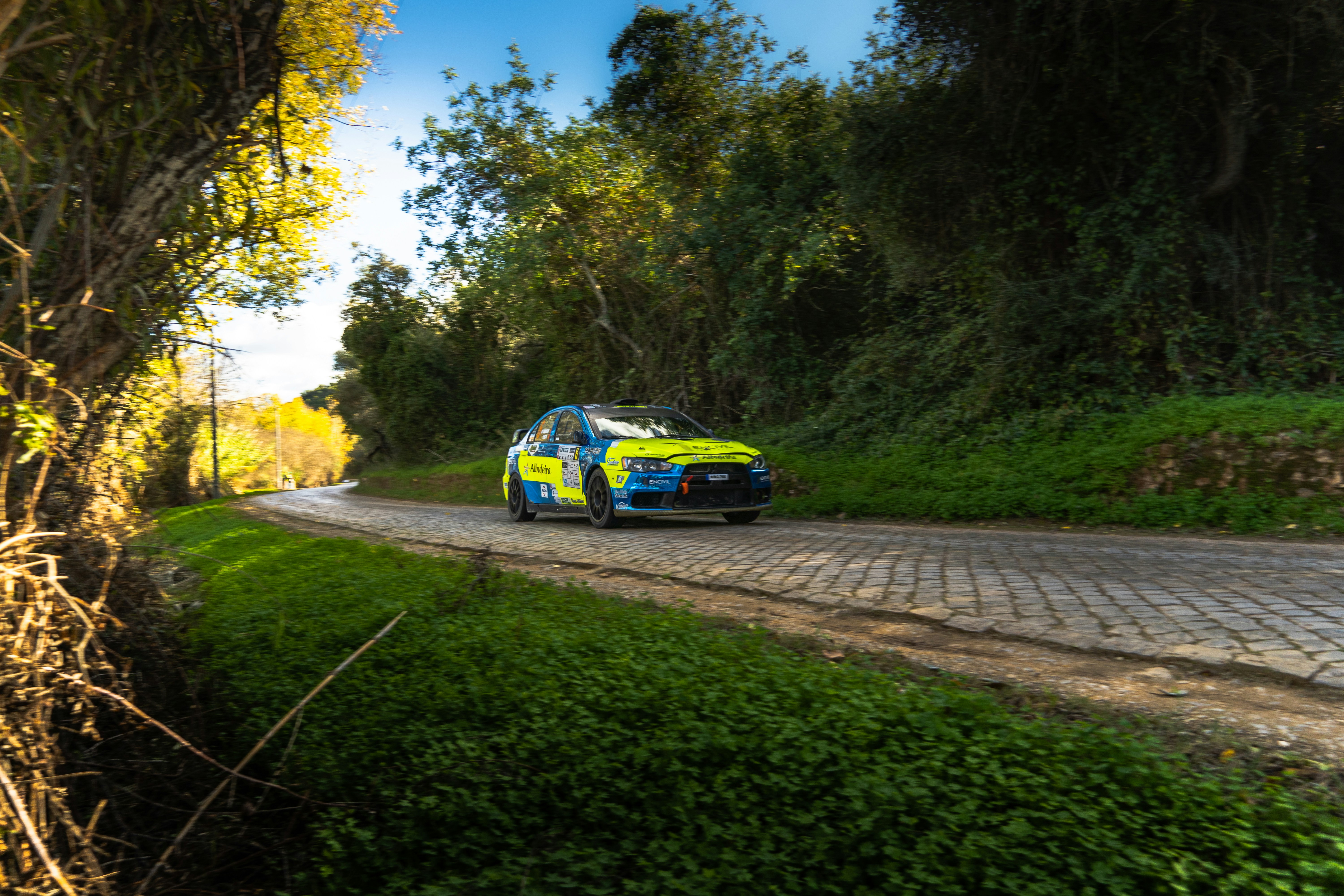 Blue-and-Yellow Police Car Rounding a Curved Cobblestone Road