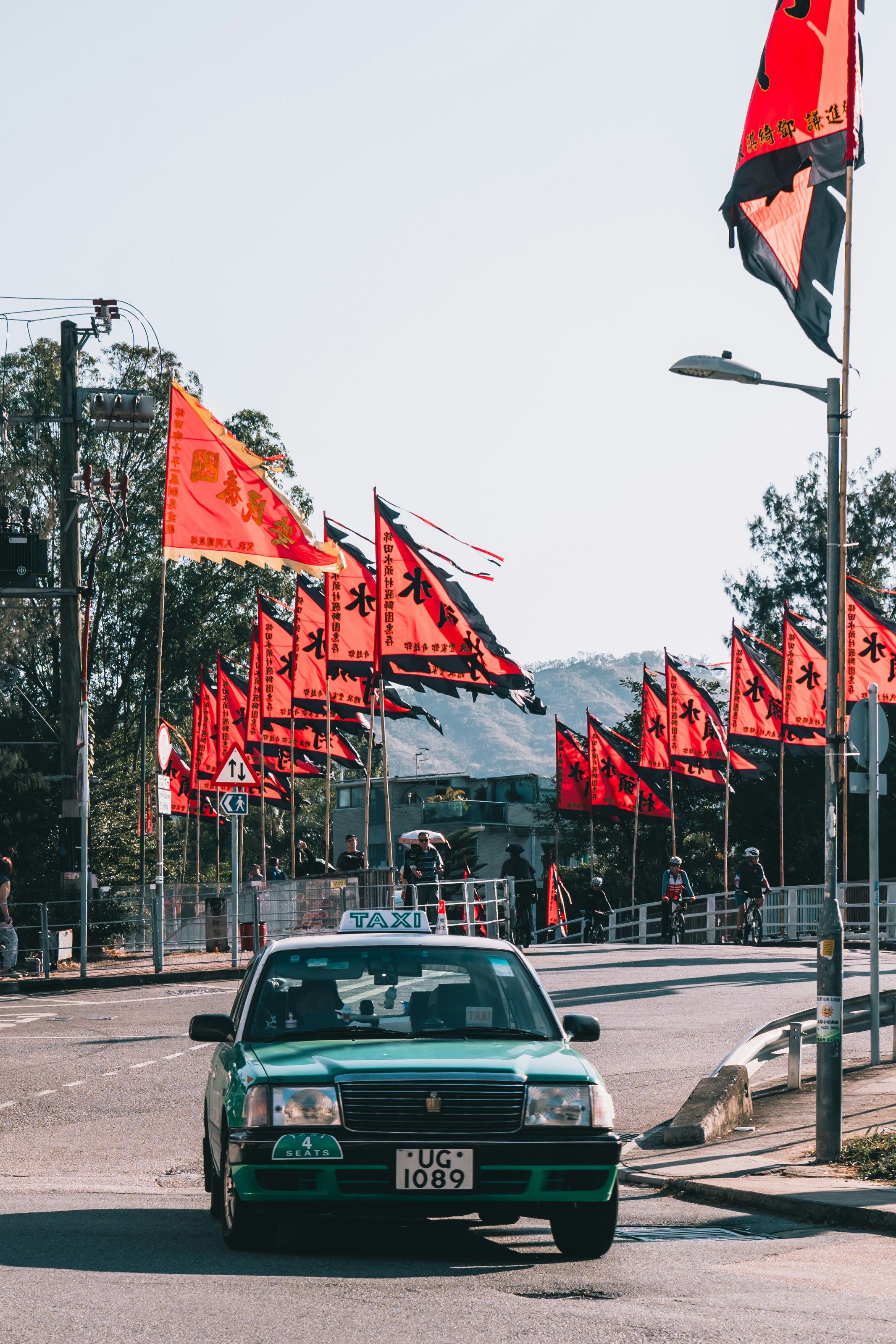 Green Taxi on a Flag-Flanked Street at Distant Rally