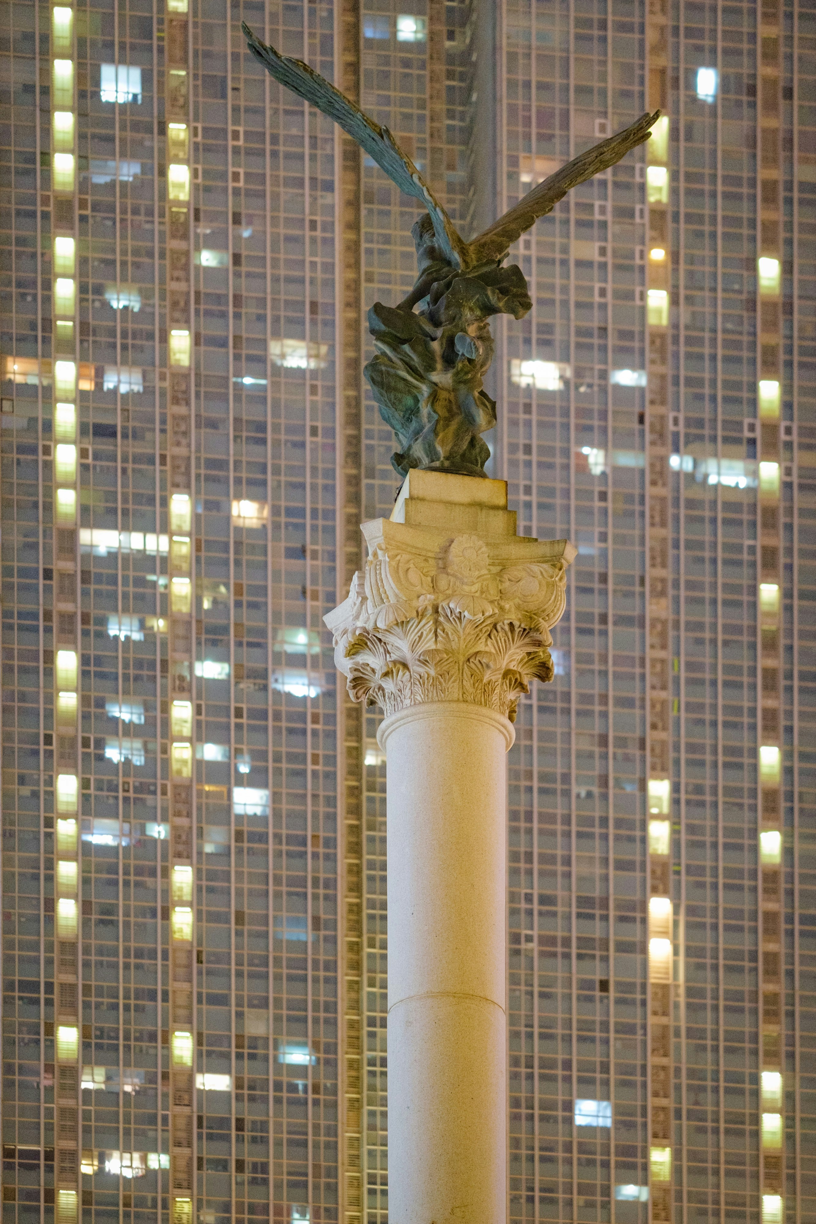 Winged Guardian Above the Column: Nighttime Monument Against City Grid