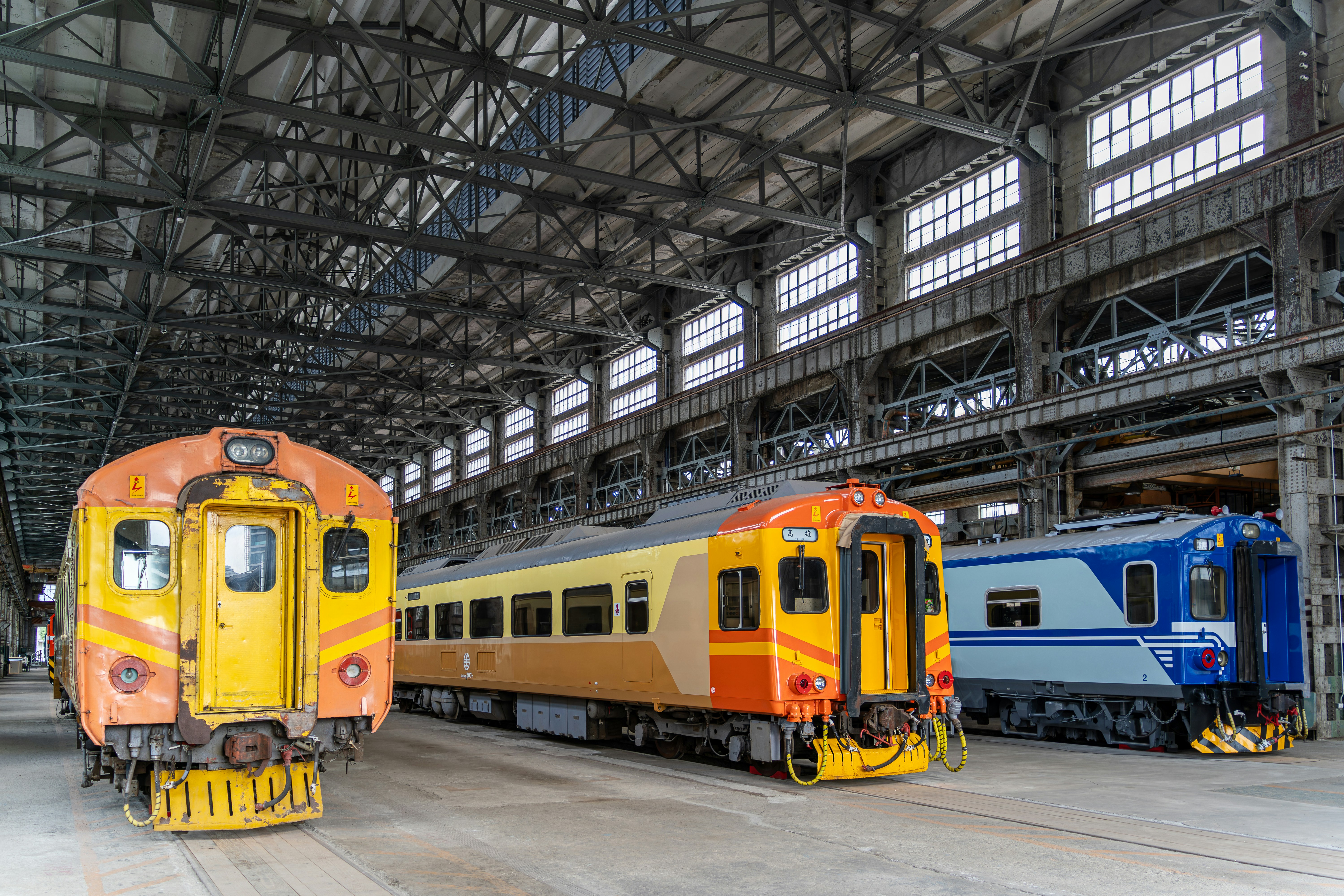 Three colorful trains parked inside a large industrial building. photo ...