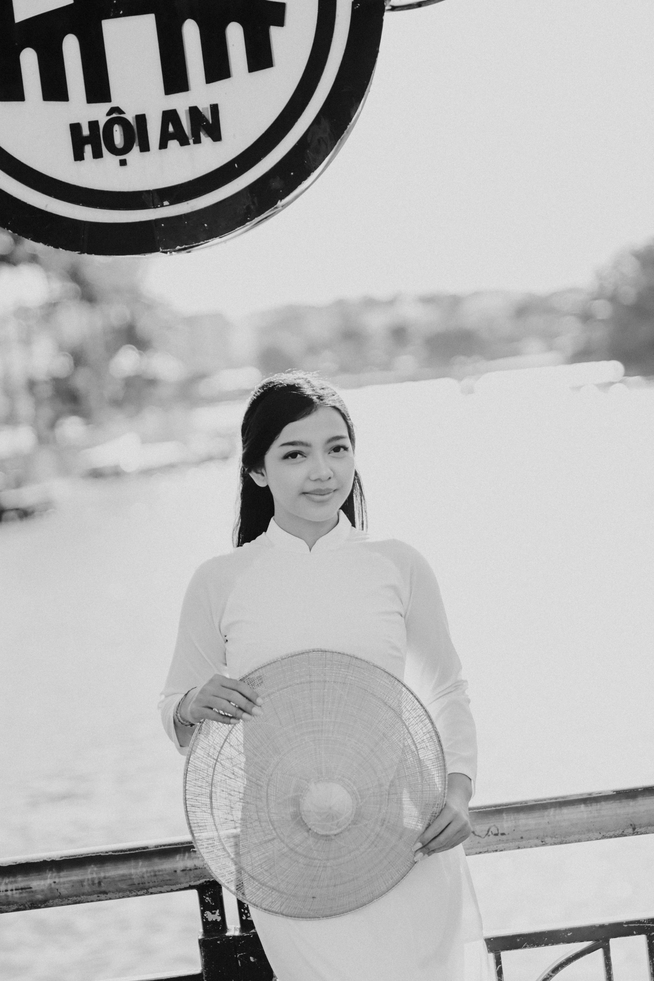 Portrait by the Water: Grace in a White Ao Dai Holding a Circular Conical Hat