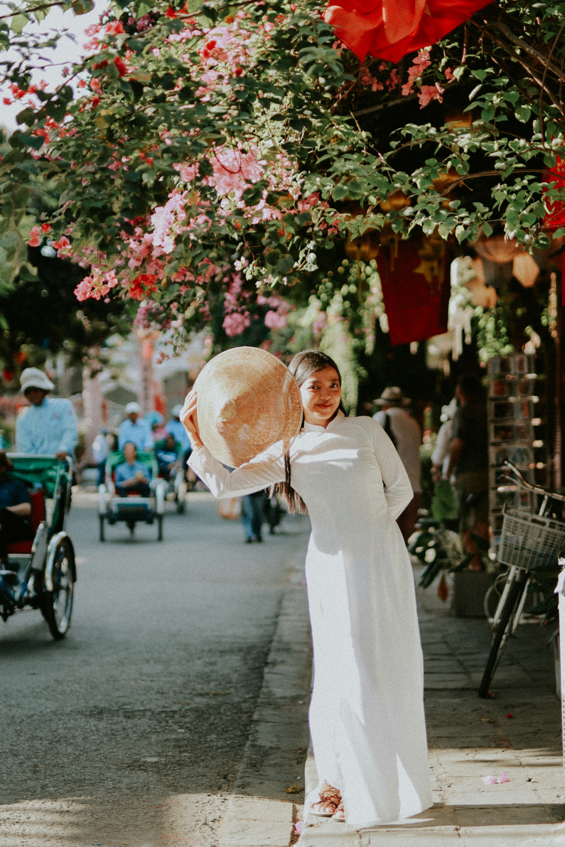 White Áo dài under flowering arch: street portrait in a sunlit doorway