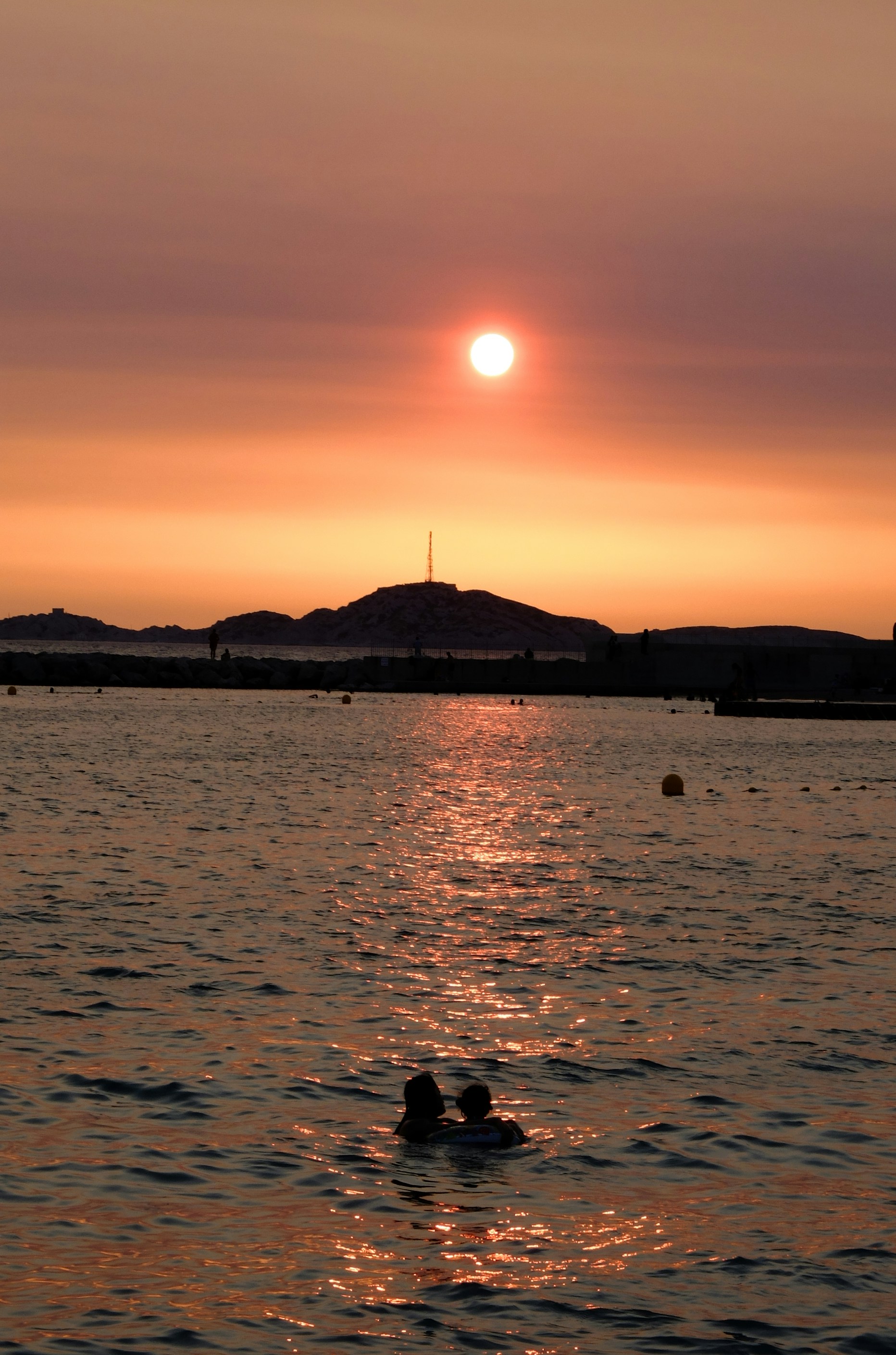 Sunset Silhouette over Quiet Bay with Two Figures in the Water