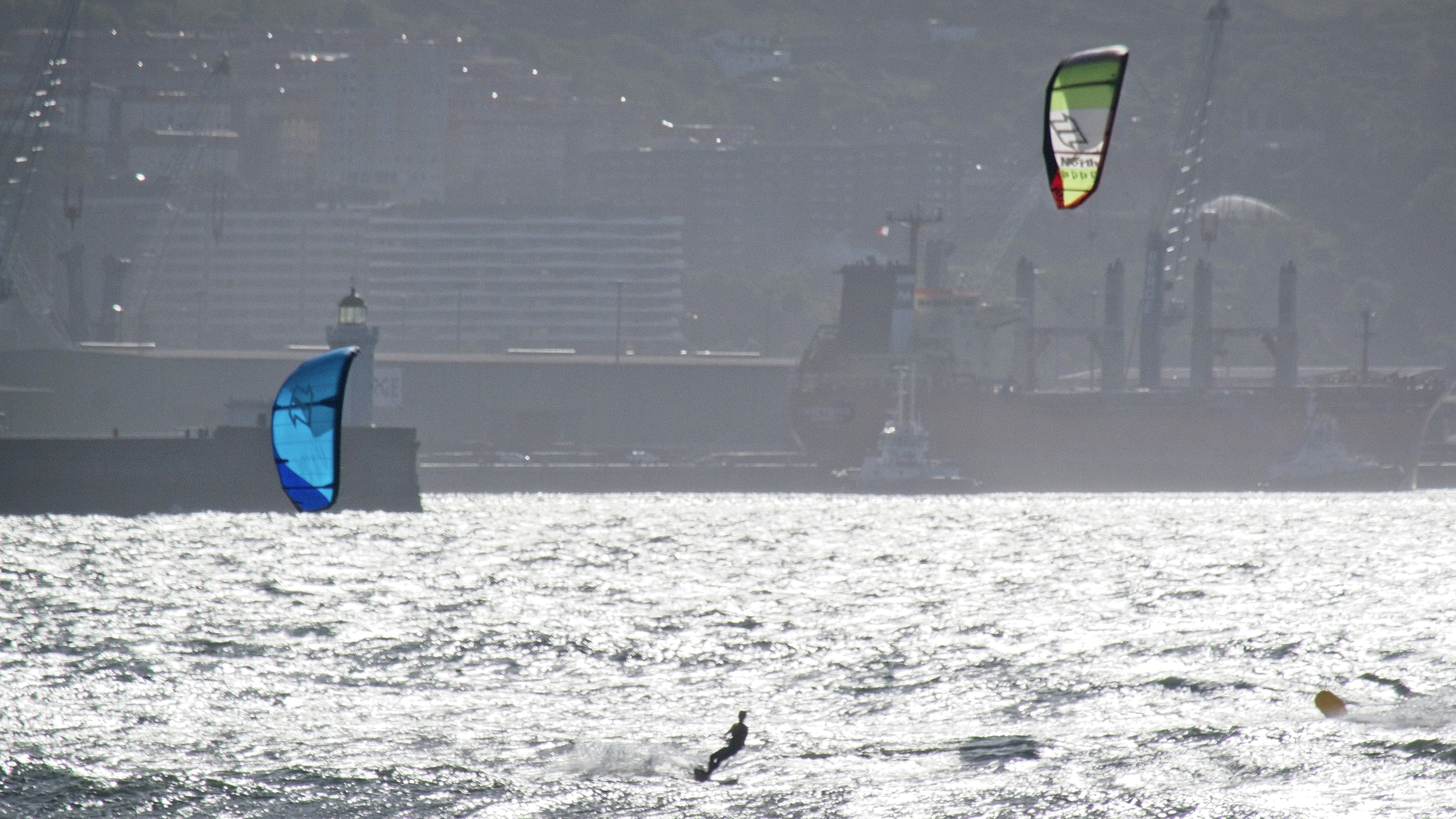 Windswept Wake: Kiteboarders Glide Across a Shimmering Harbor