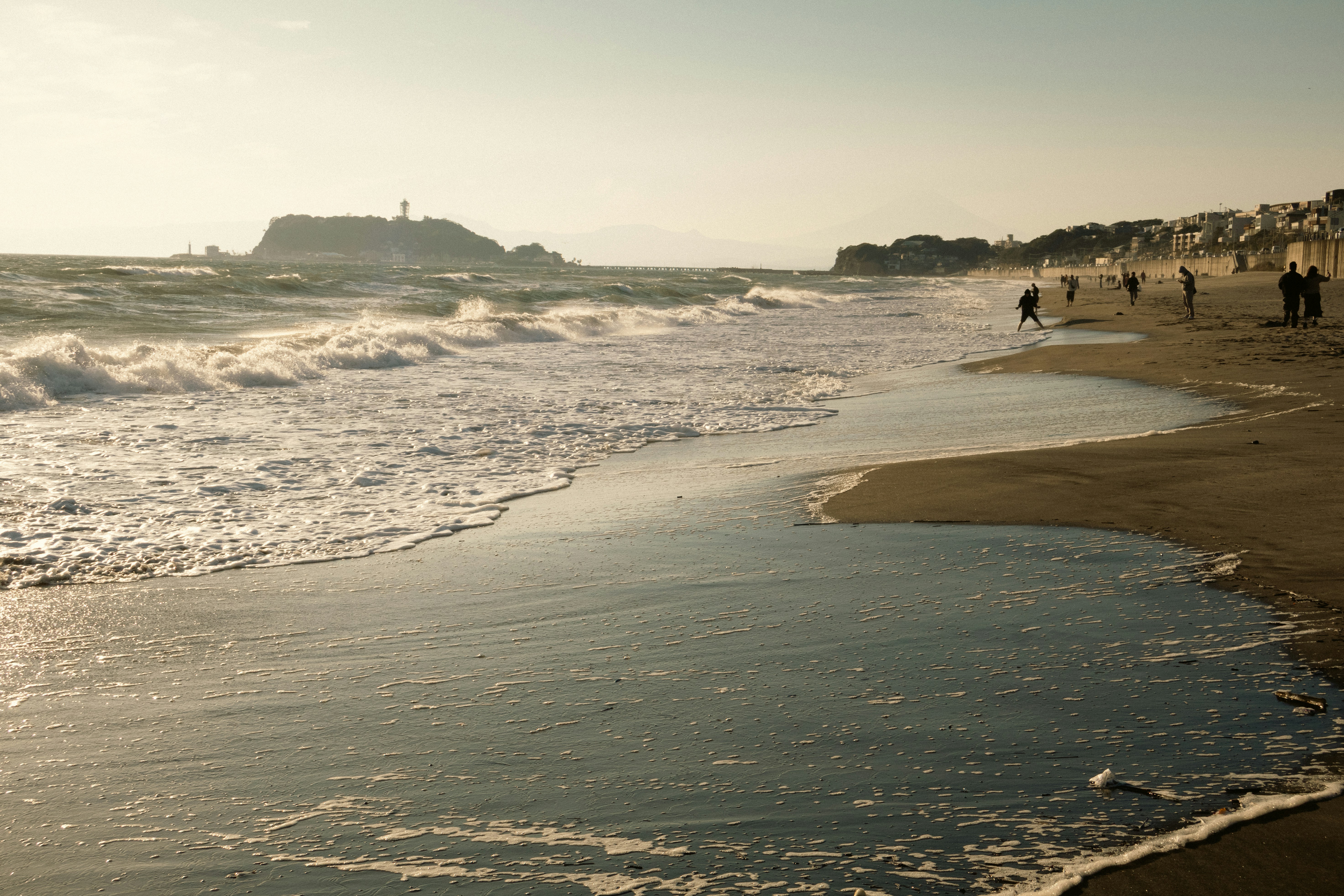 Sunlit shoreline with distant headland and beachgoers