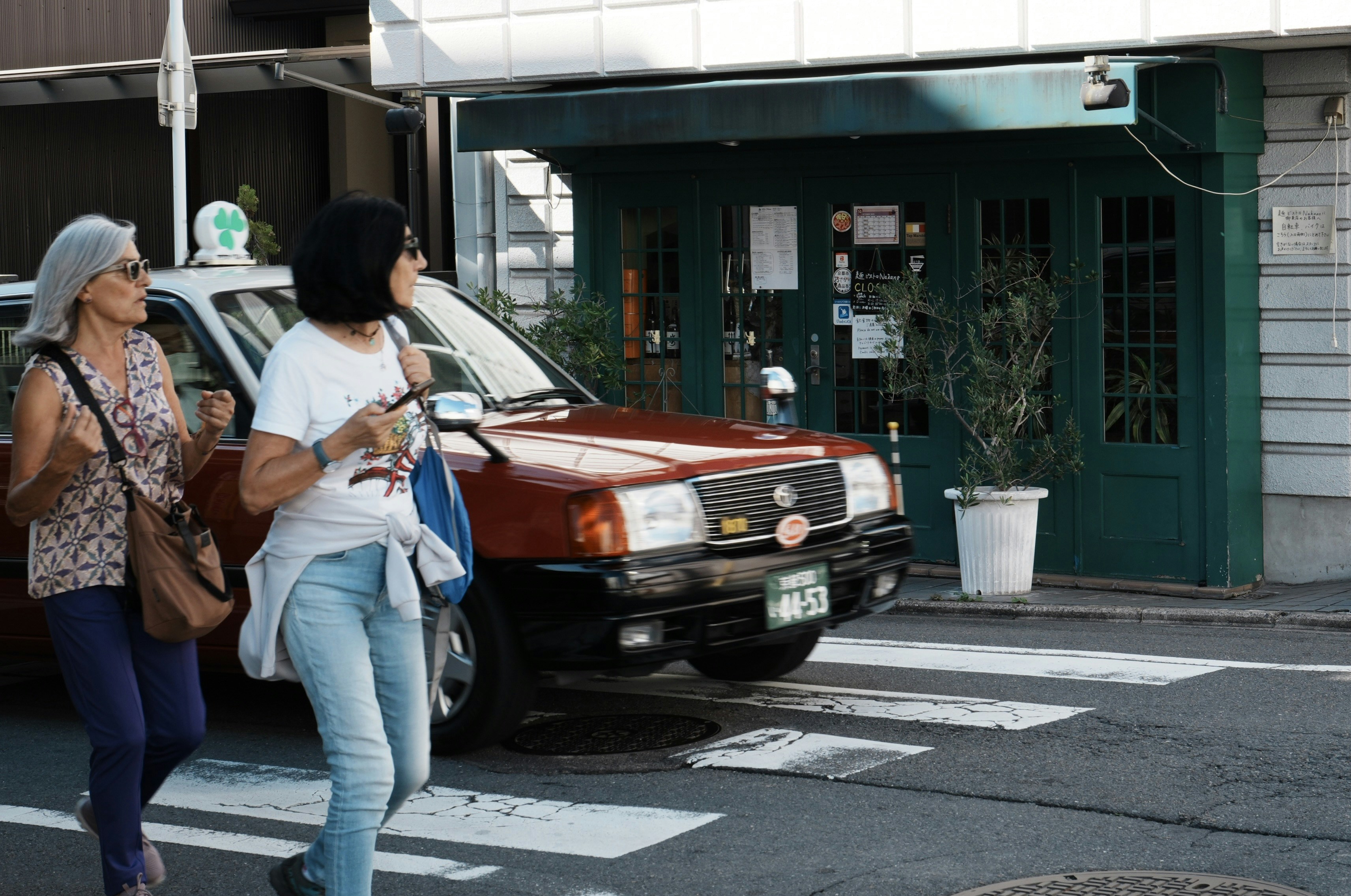 City Crossing in Focus: Two Women Walk the Crosswalk as a Car Pauses