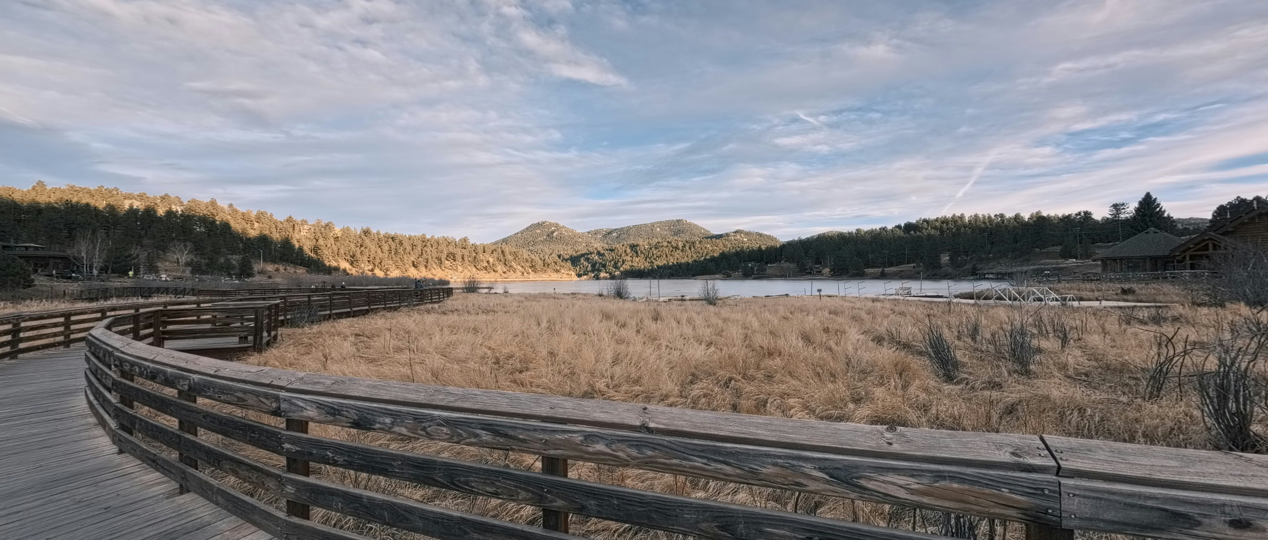 Wooden boardwalk curves around dry grass near a lake.