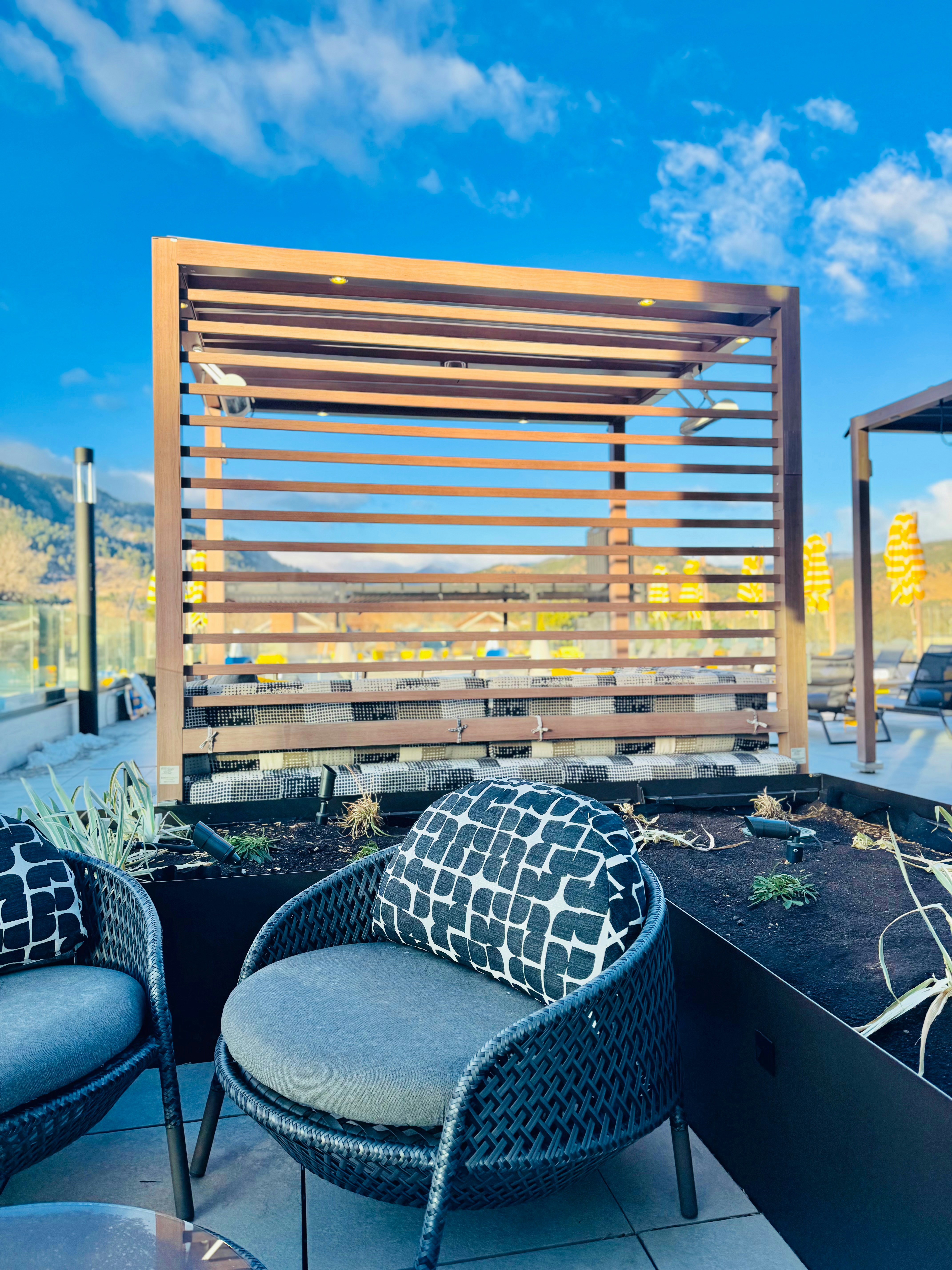 Shaded lounge beneath a louvered pergola overlooking sunlit resort furniture
