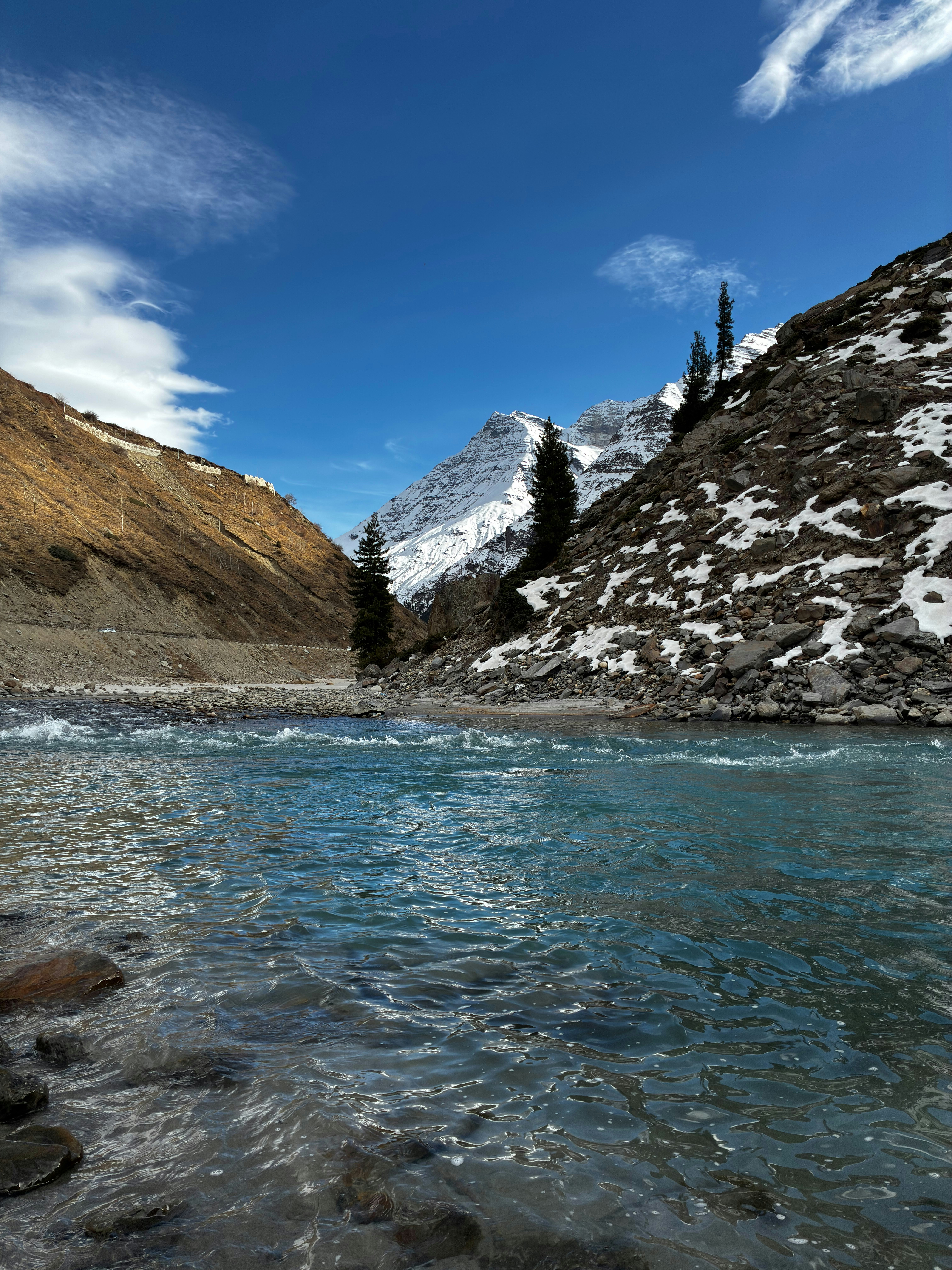 Blue river flows through snowy mountains under a clear sky.