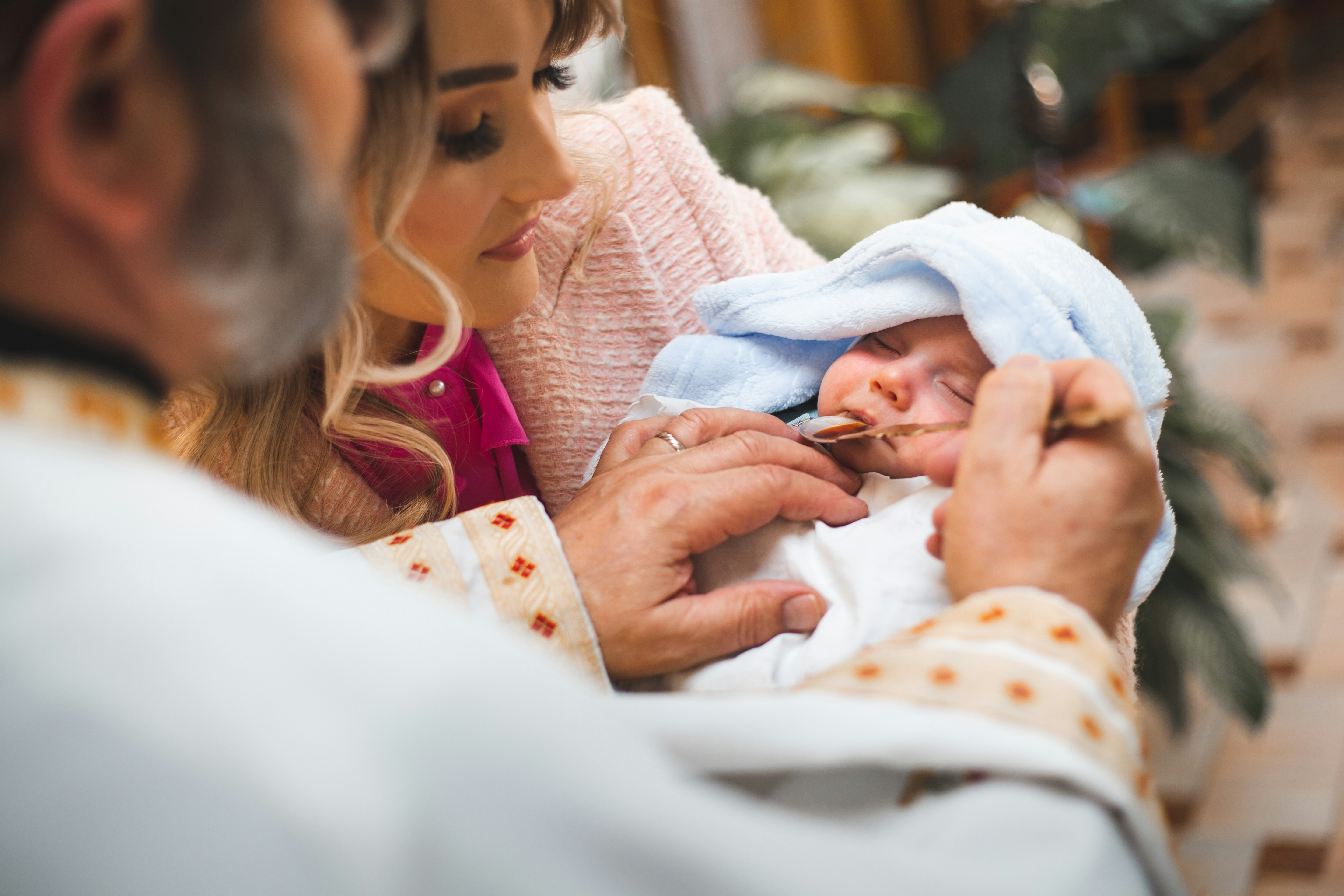 Mother holding her young baby boy, while the priest give him the holy communion.