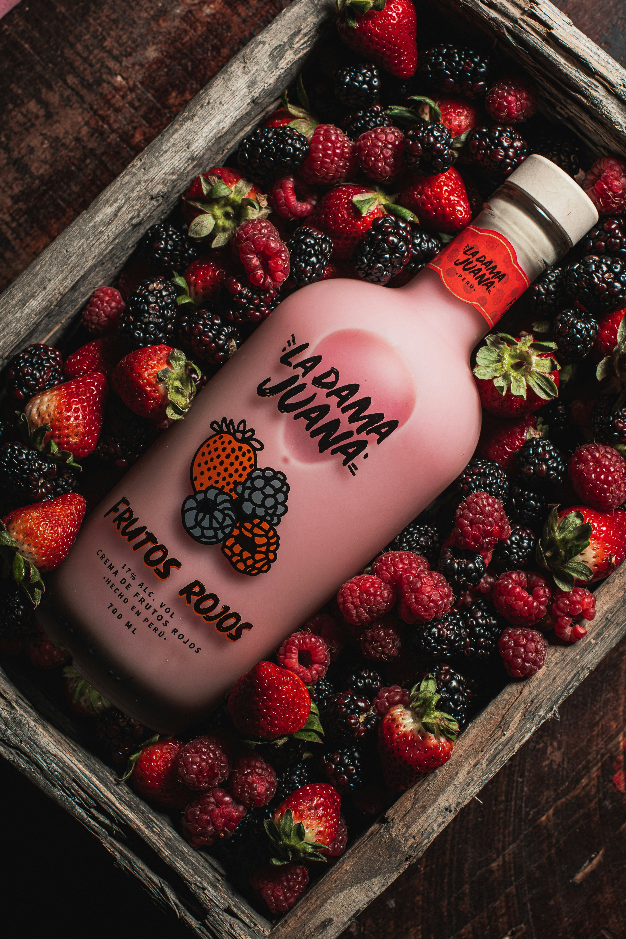 Pink bottle of Adamá Juana among a berry harvest in a wooden crate