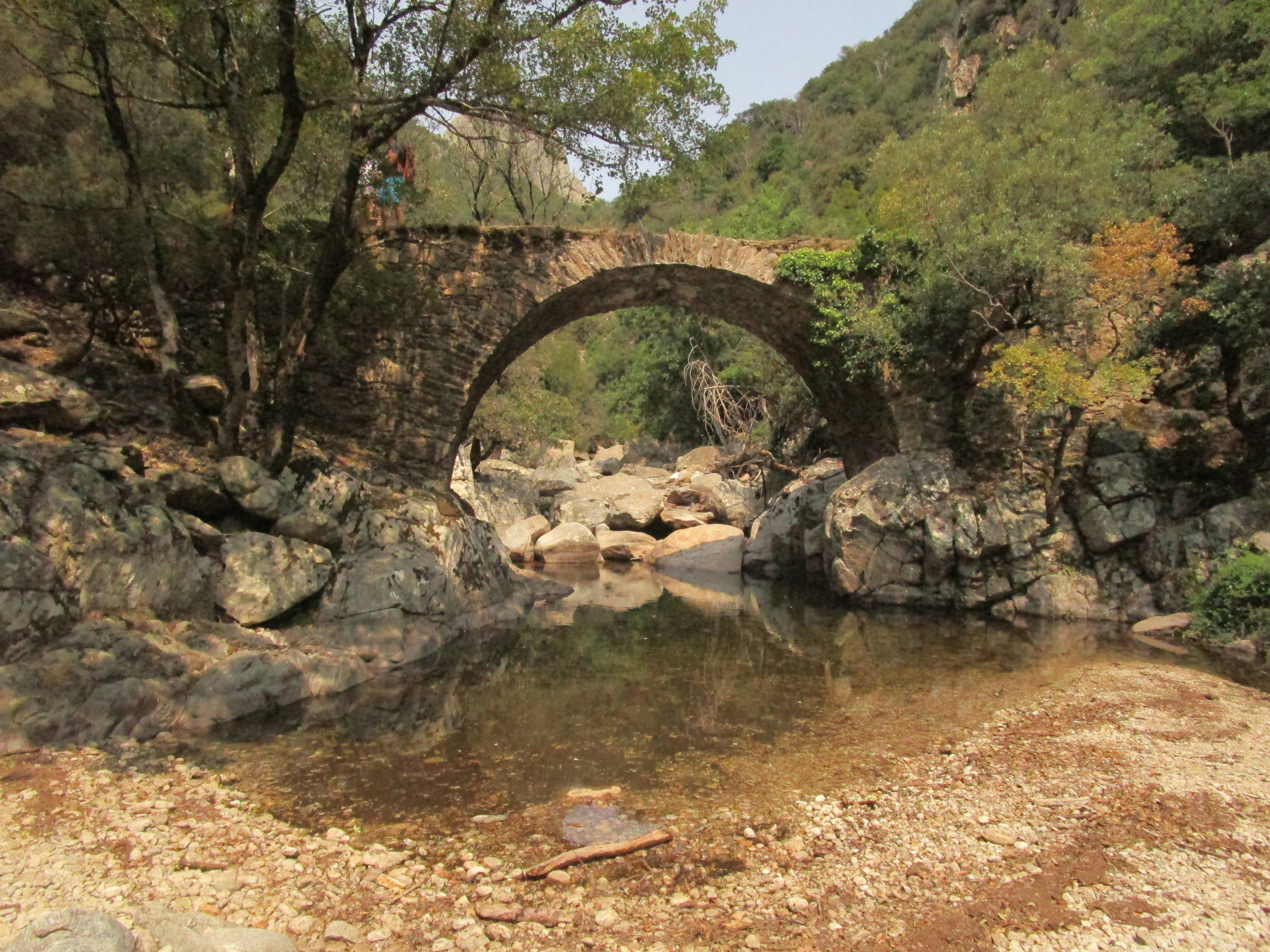 An old stone bridge arches over a shallow river.