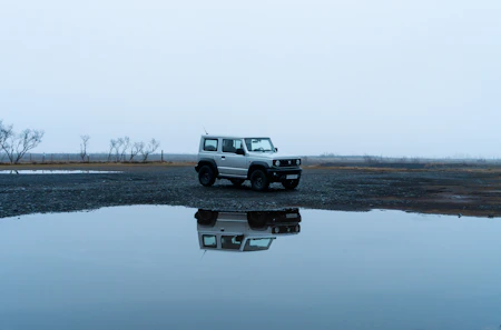 White SUV on a silent shoreline, mirrored in a still tidal pool