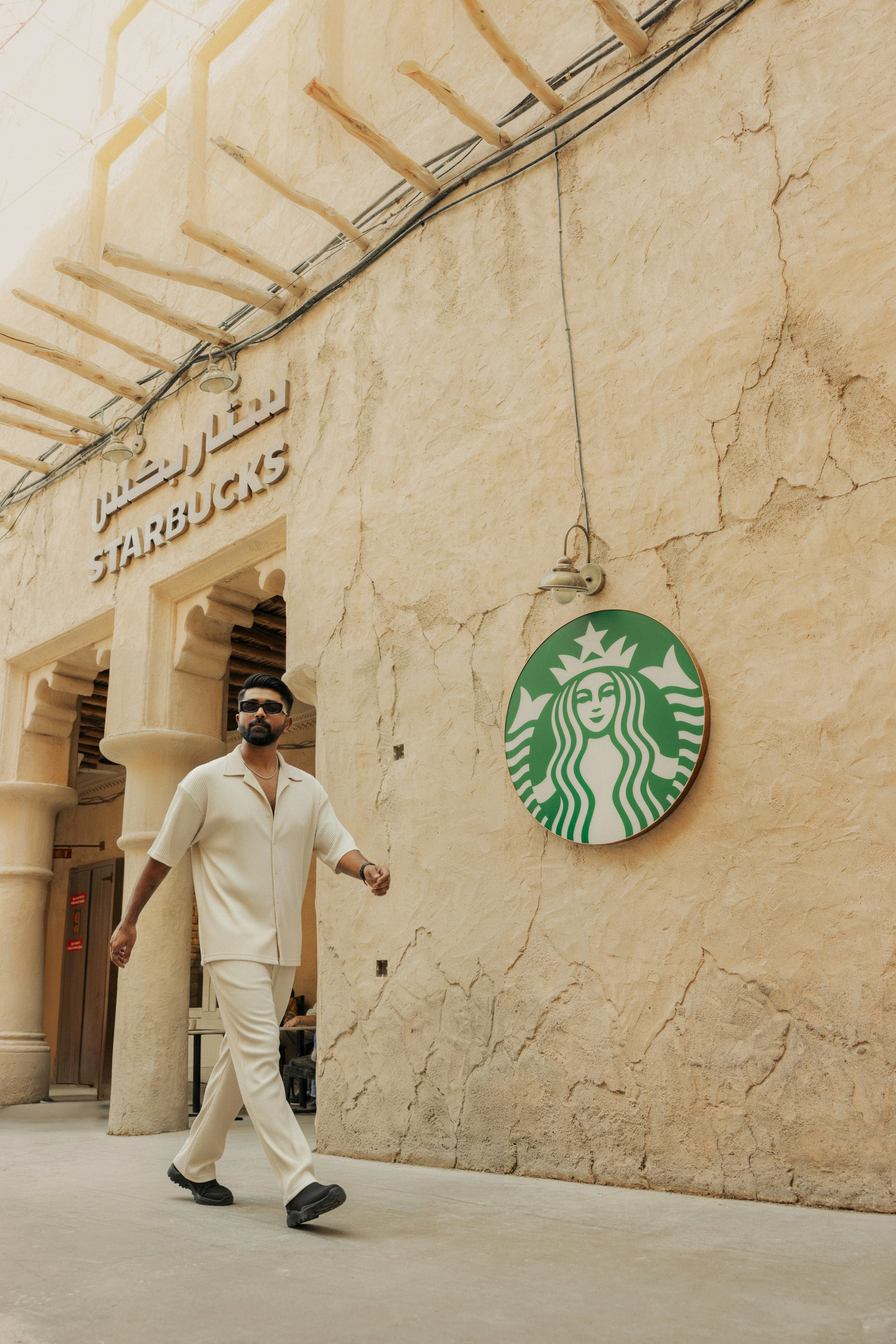 Casual stride past a sunlit Starbucks storefront in sandy tones
