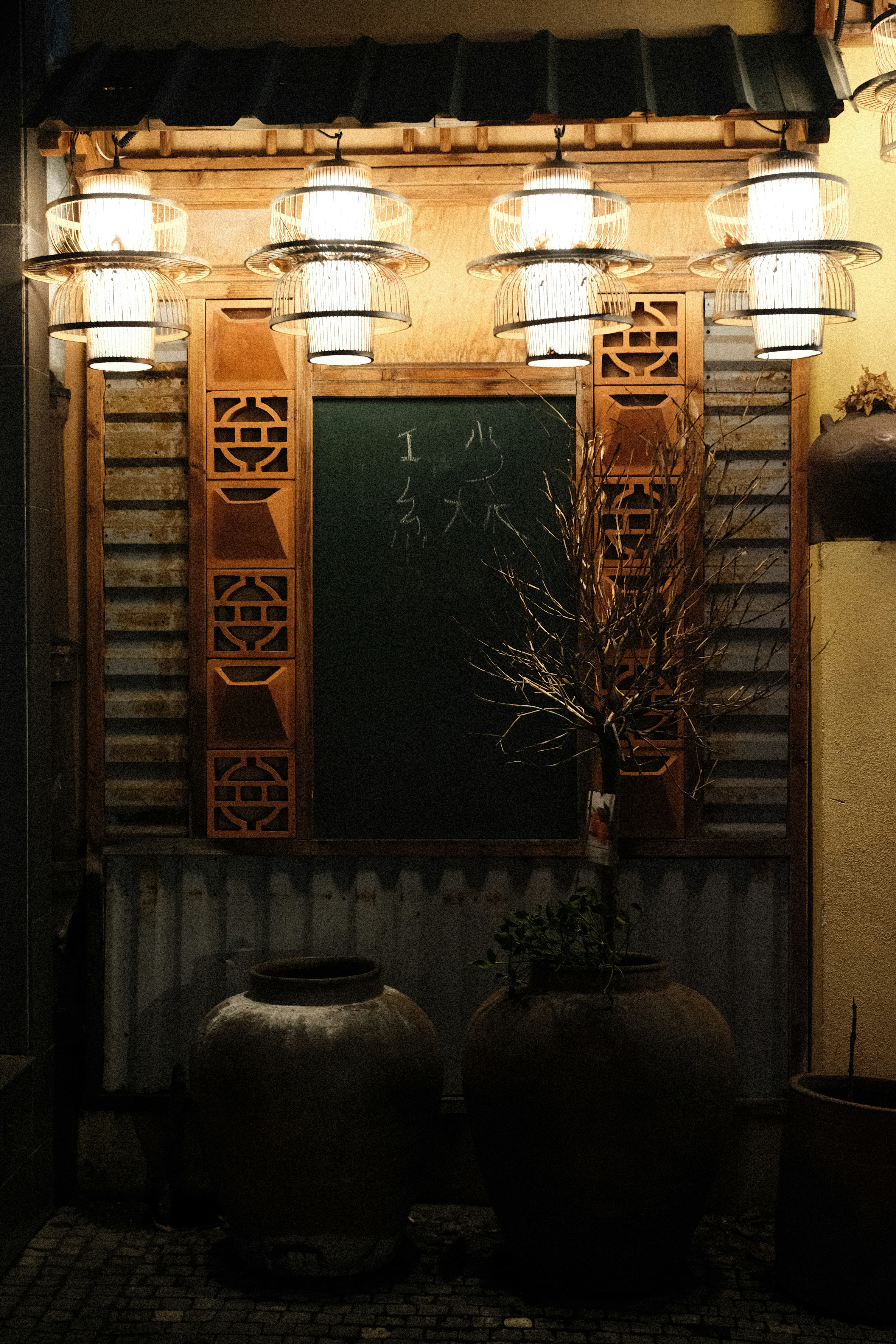 Lantern-lit doorway with ceramic pots and bare tree silhouette