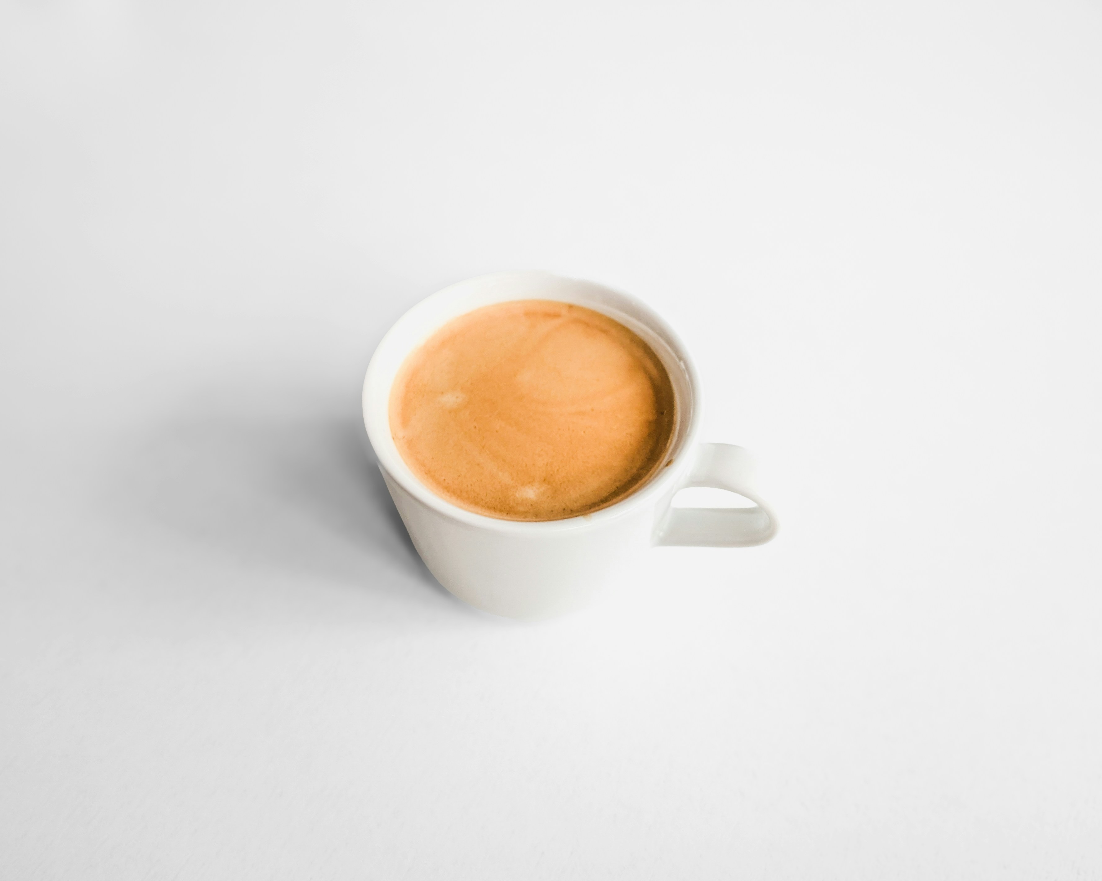 A white mug filled with coffee on a white surface