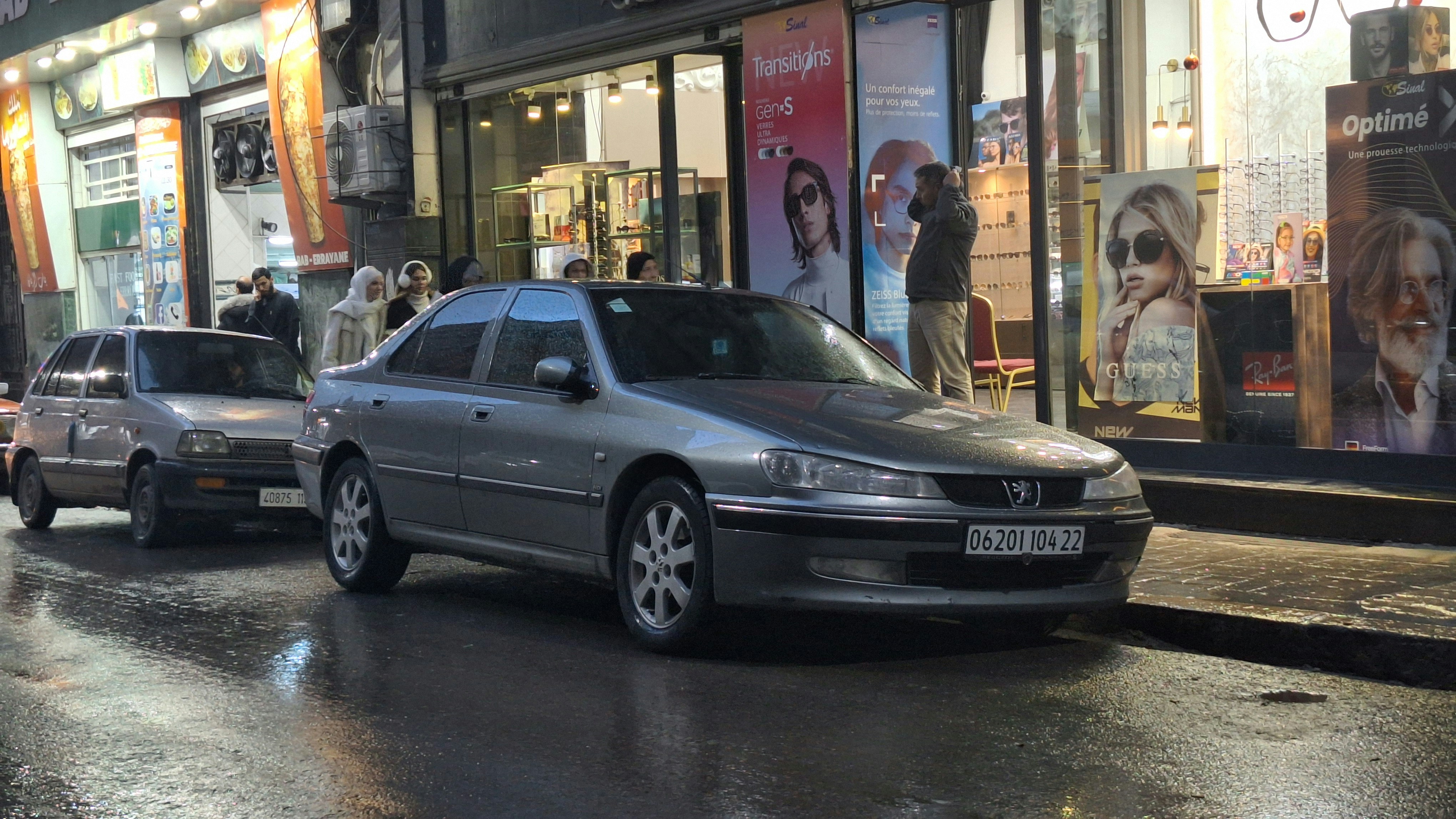 Oncoming City Street: Silver Sedan Under Neon Shopfronts