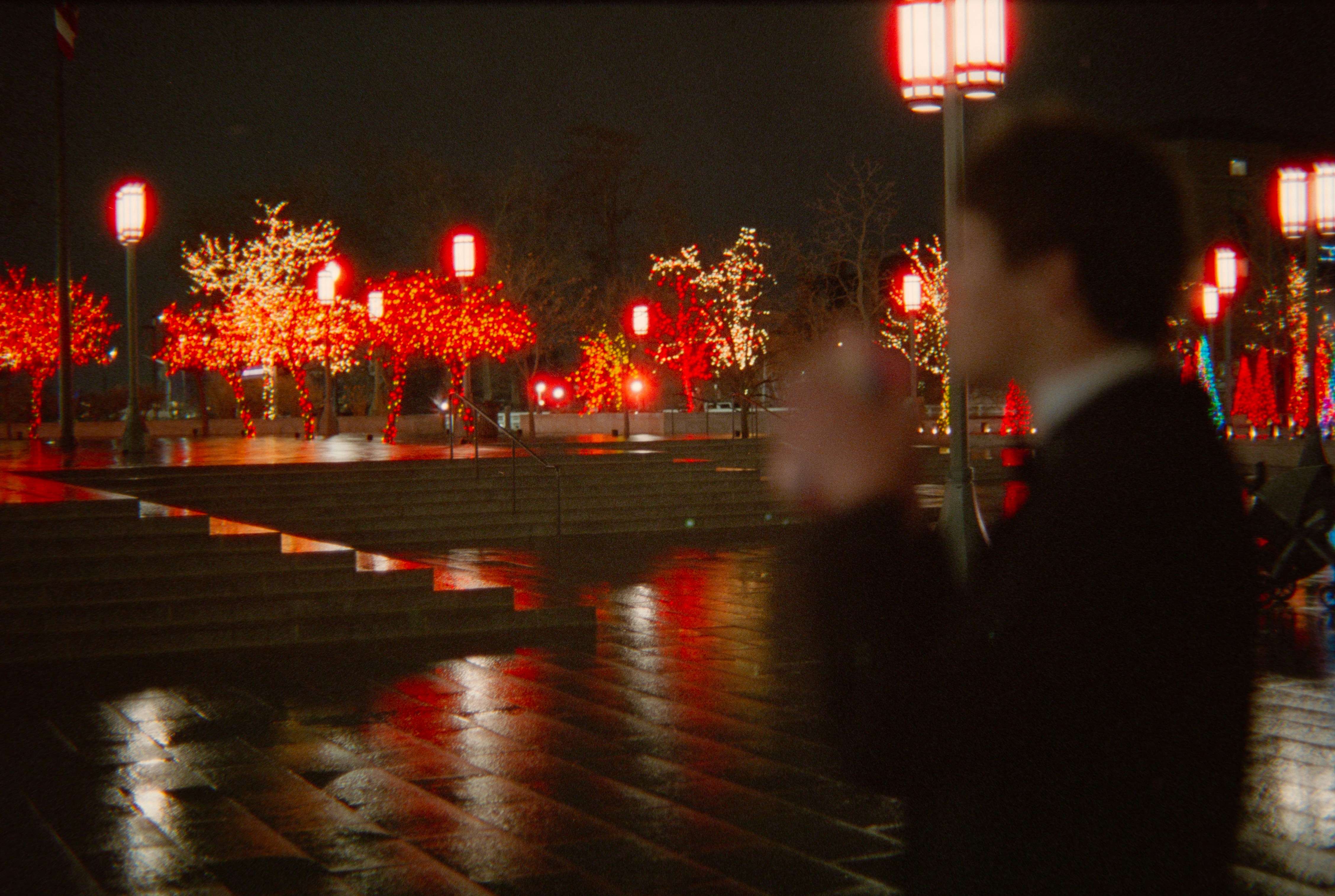 Blurred silhouette beside glowing lanterns in a rain-soaked night park