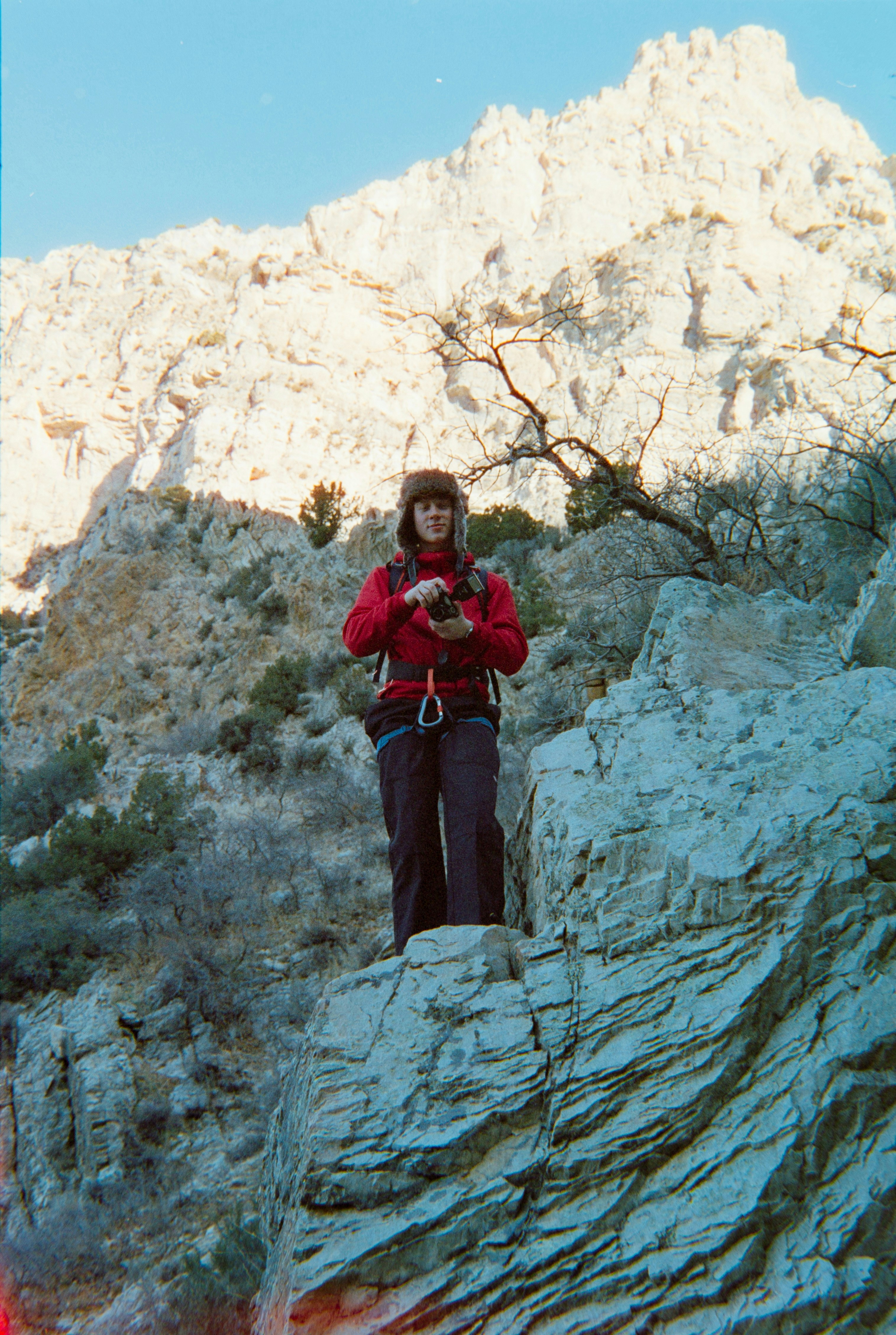 Climber in Red Jacket Anchored on a Rugged Cliff