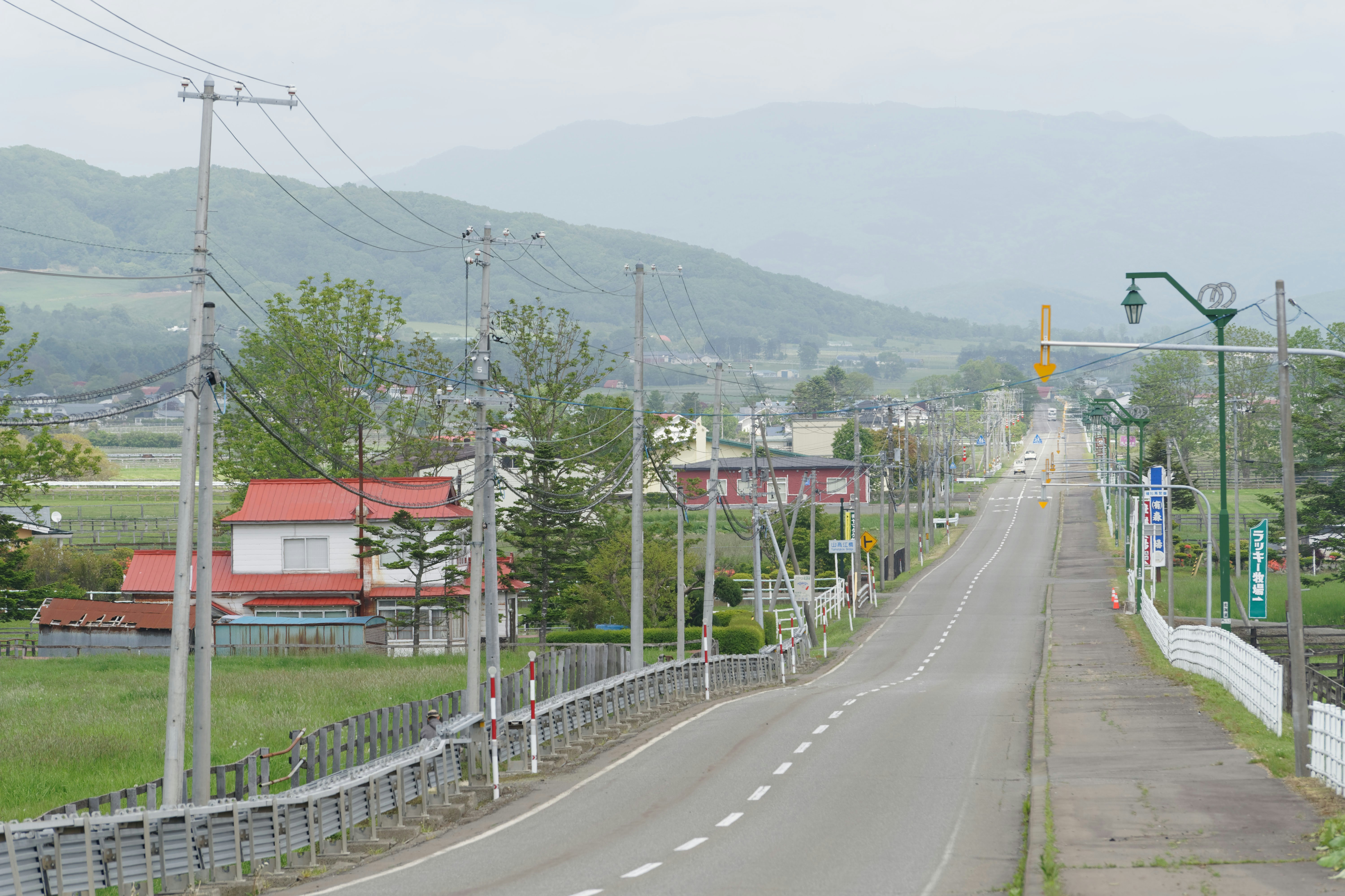 Rural road leading to a small town with hills.