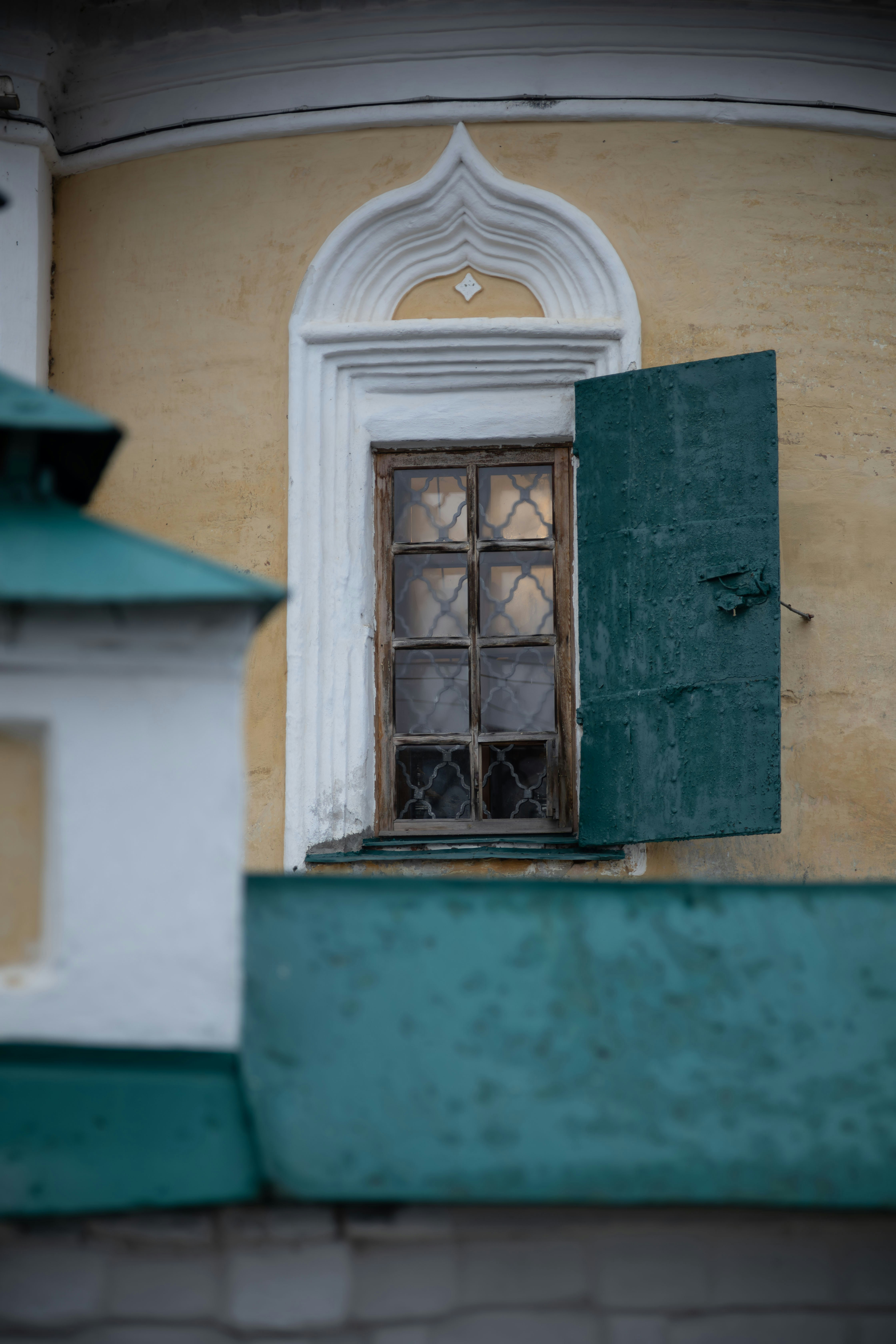 Teal shutter over a sunlit arched window