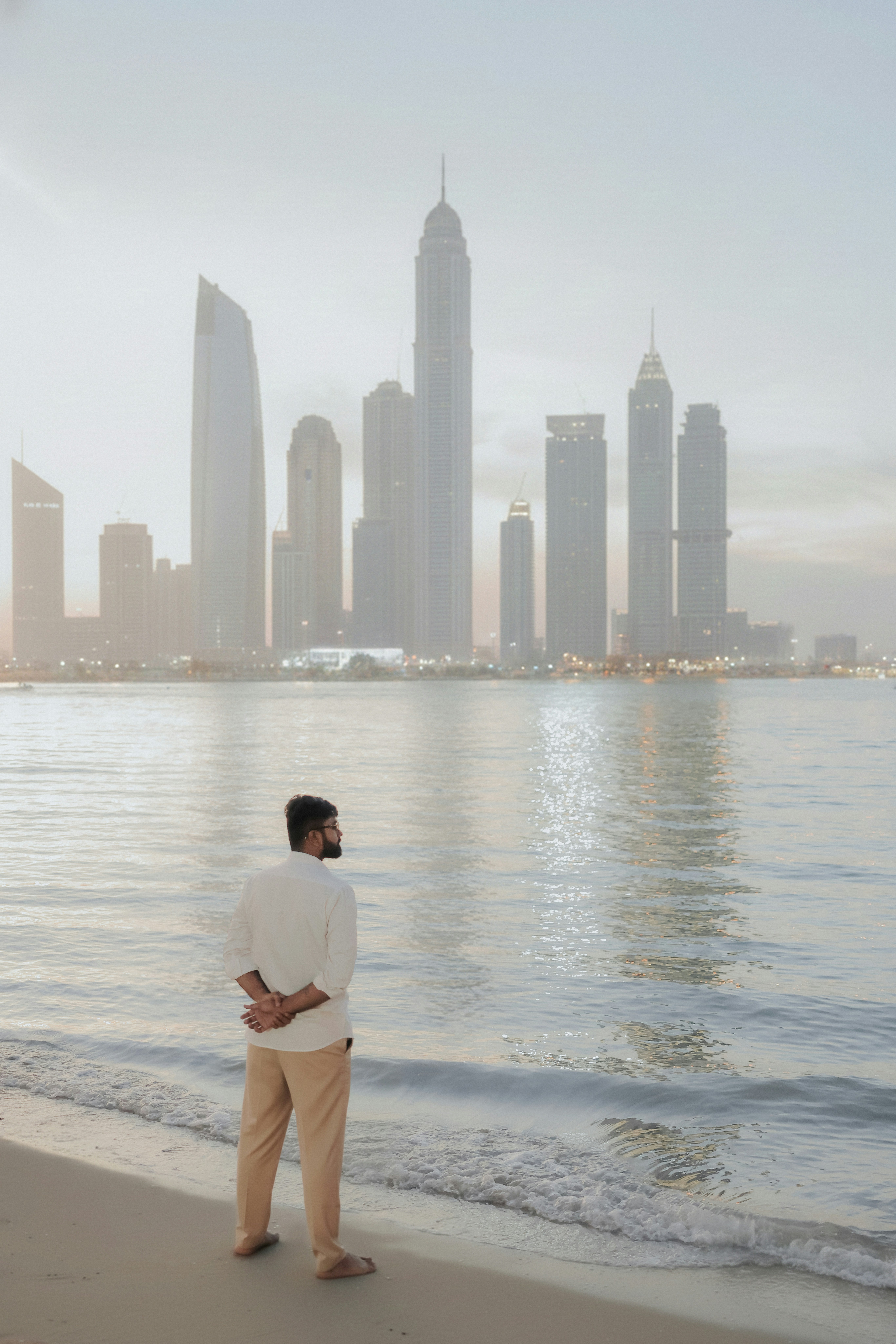 Lone Figure by the Shoreline with a Shimmering Cityscape