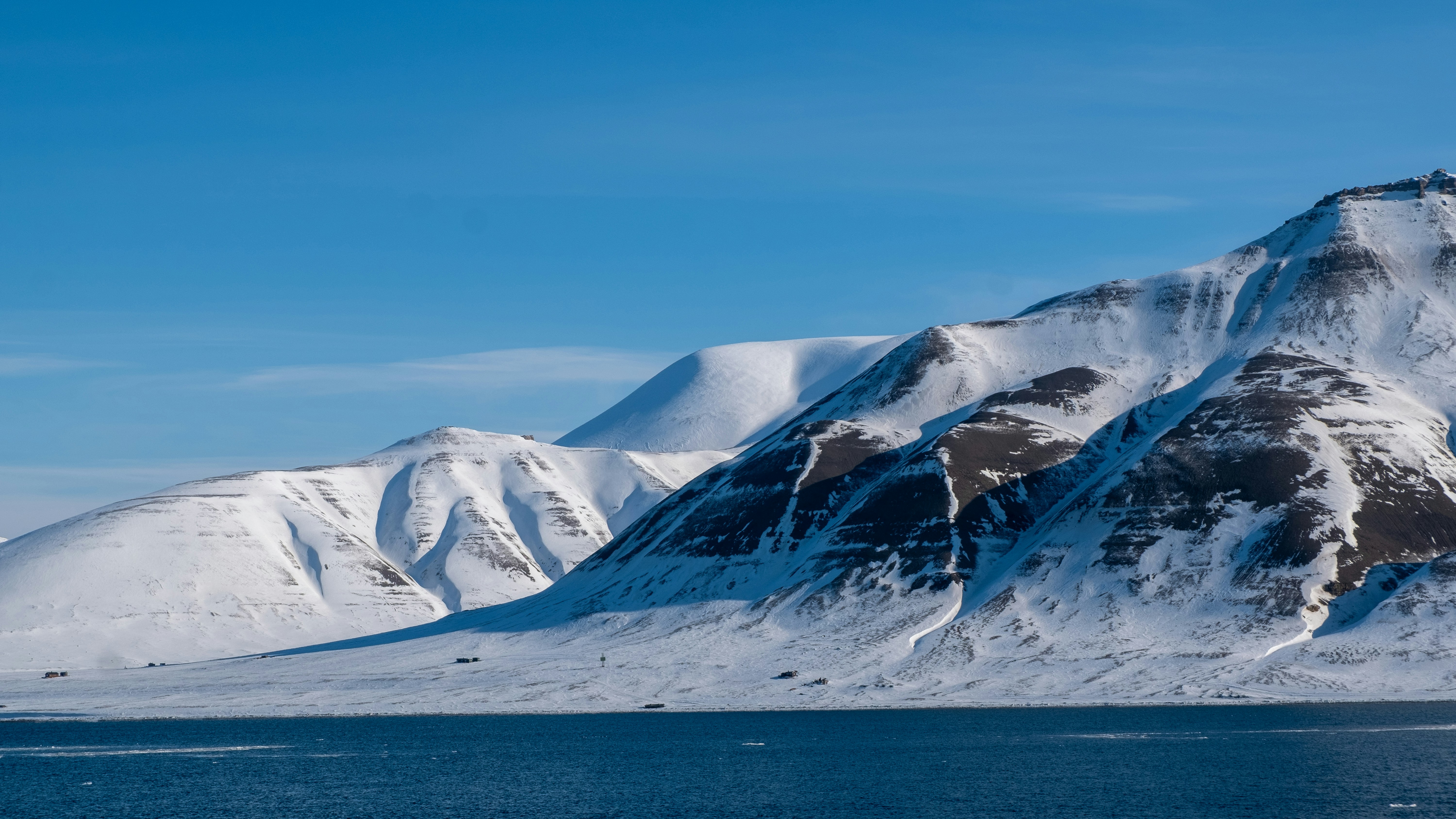 Snow-covered mountains rise above a dark blue sea. photo – Free ...