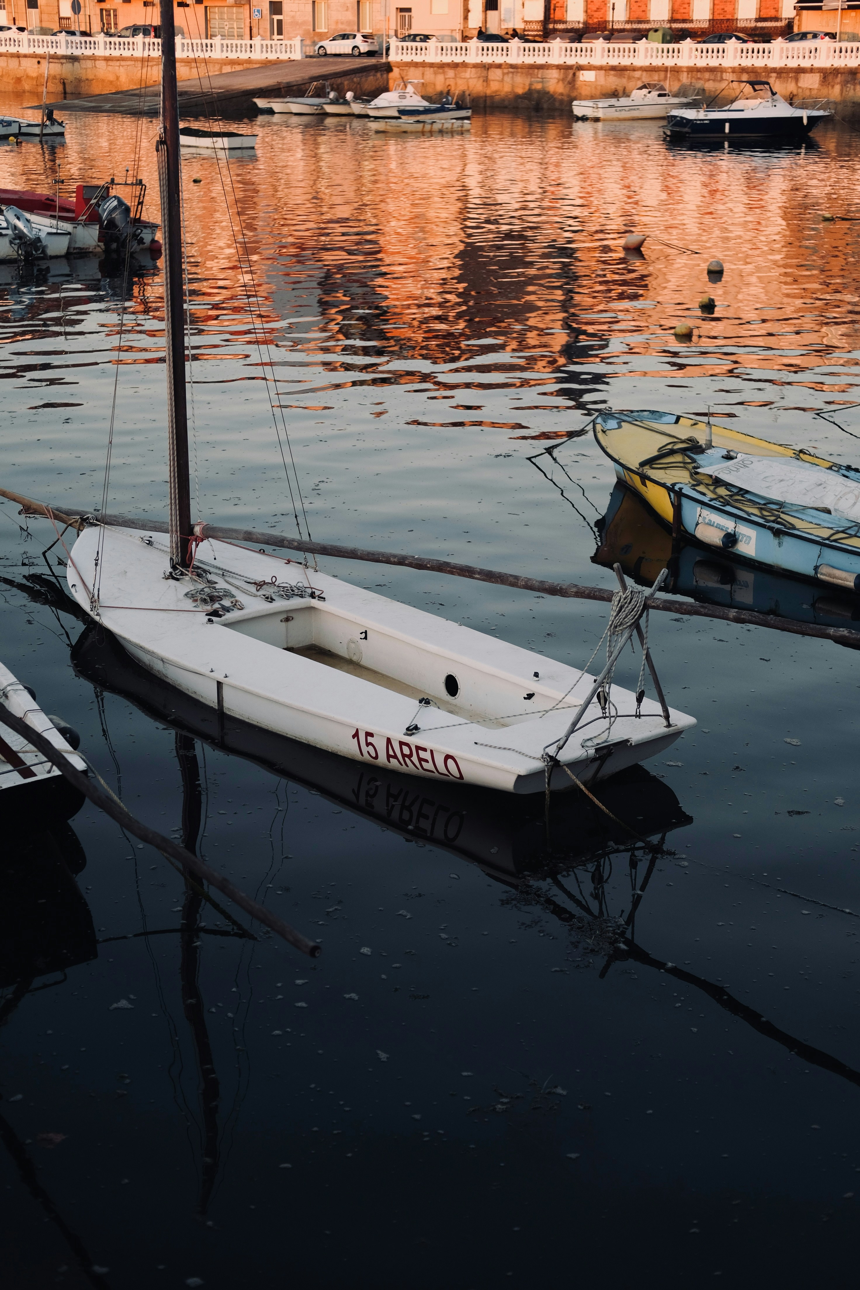 White dinghy anchored in afternoon harbor with orange-lit reflections