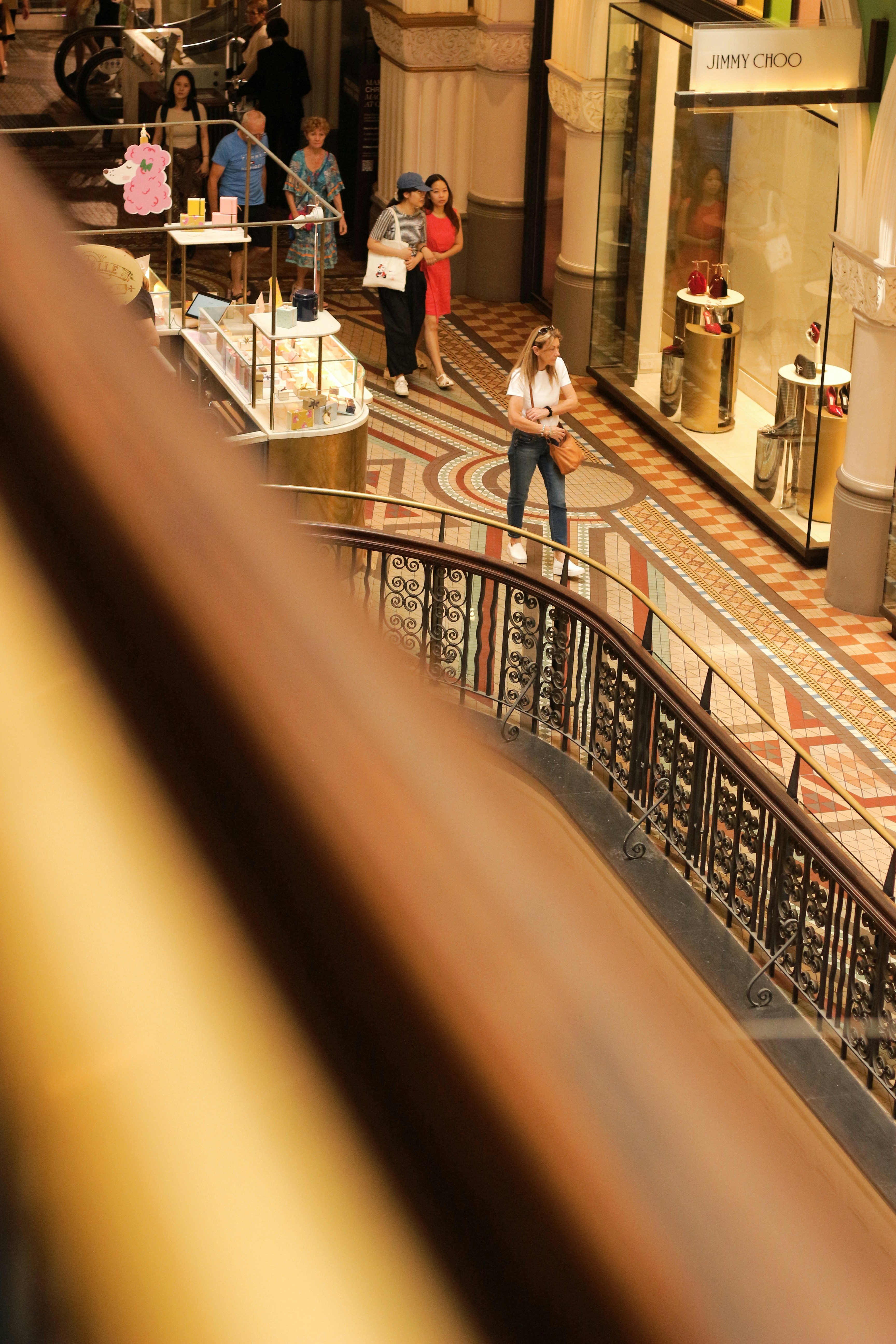 Casual shoppers in a sunlit luxury mall embrace the quiet spectacle from above