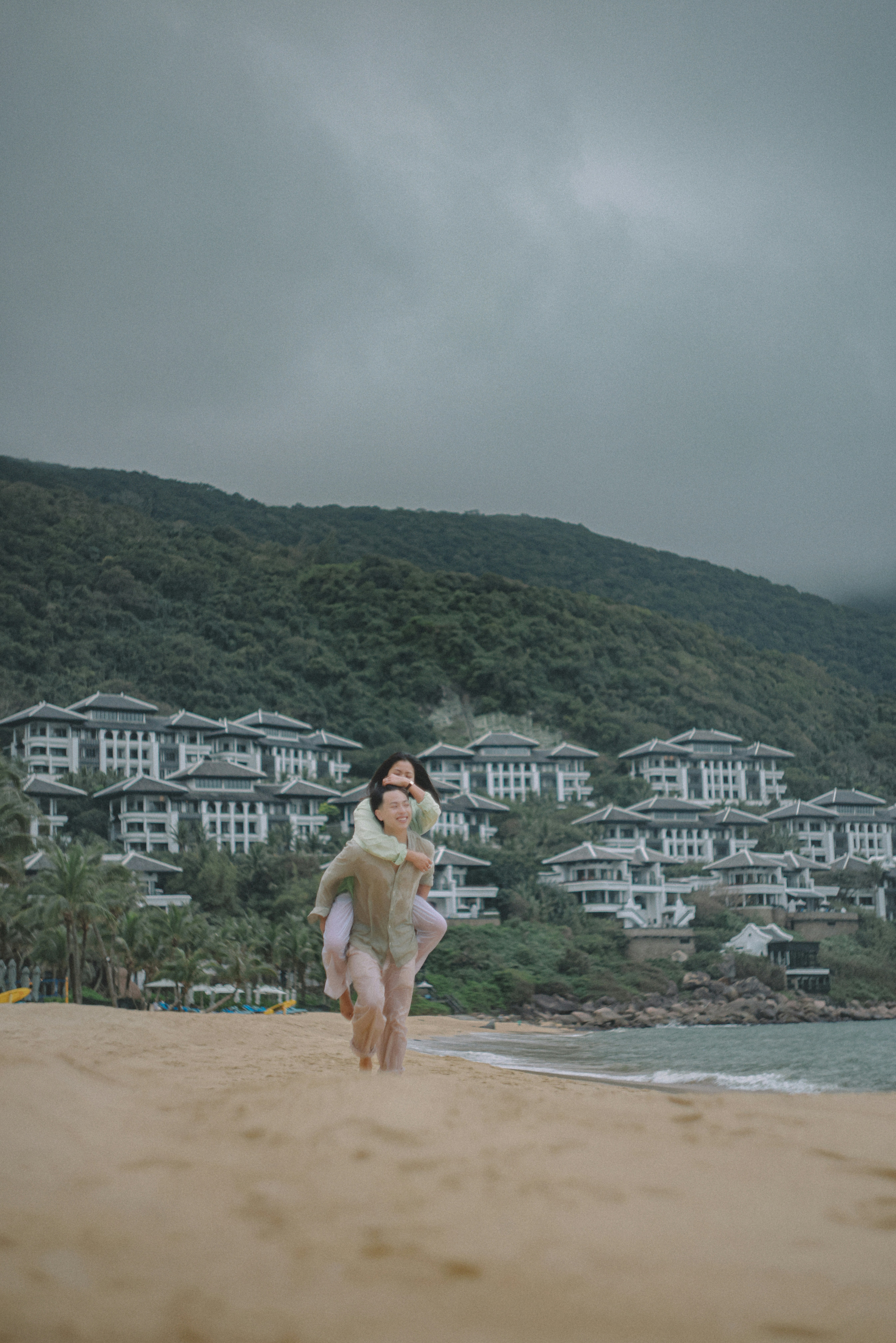 Beach Run: Mother Carrying Child Against a hillside Resort Backdrop
