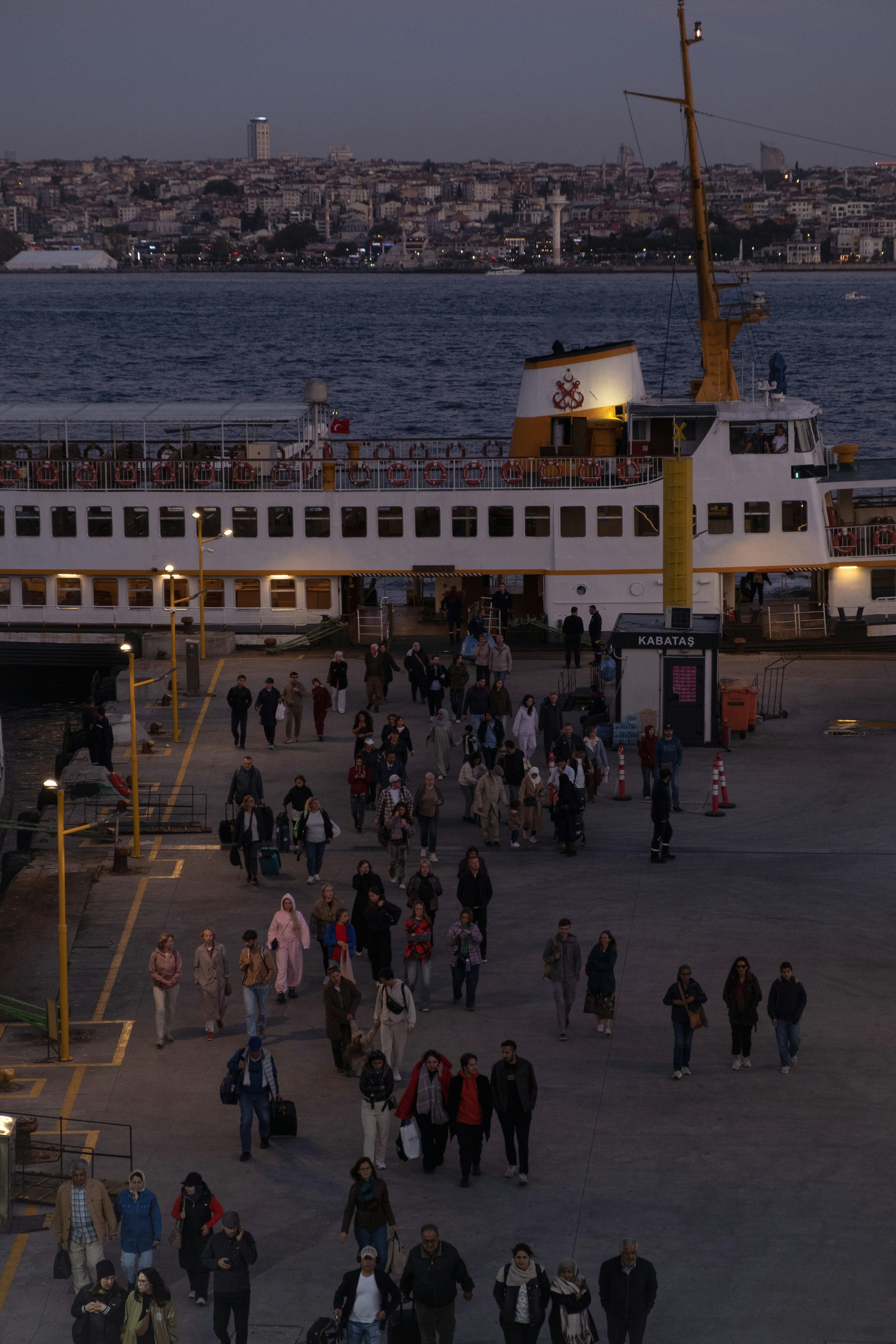 Crowded terminal at dusk: passengers descend toward the ferry as city lights wake