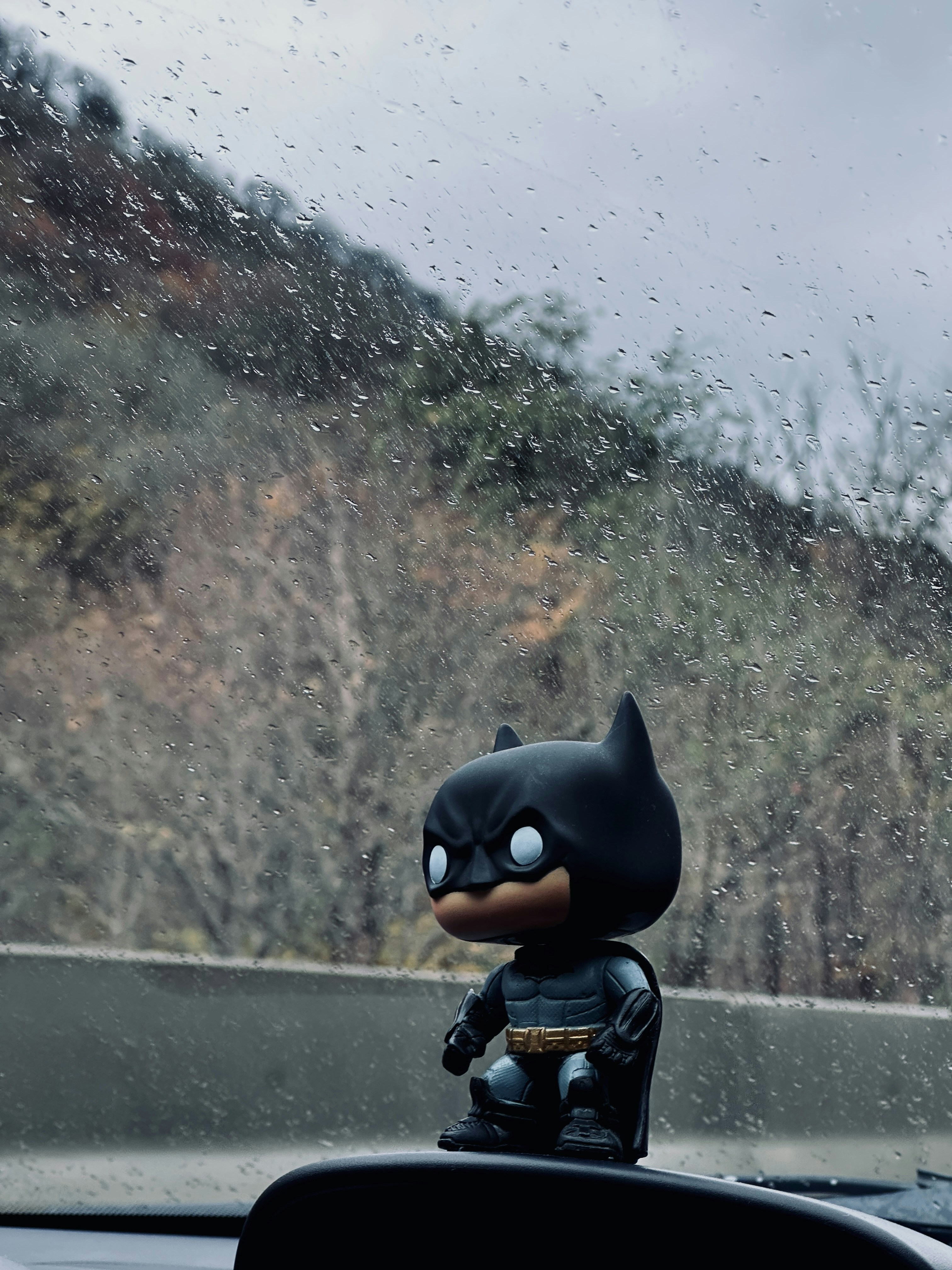 Rainy Car Windshield Guardian: Batman Miniature in a Wet Glimpse