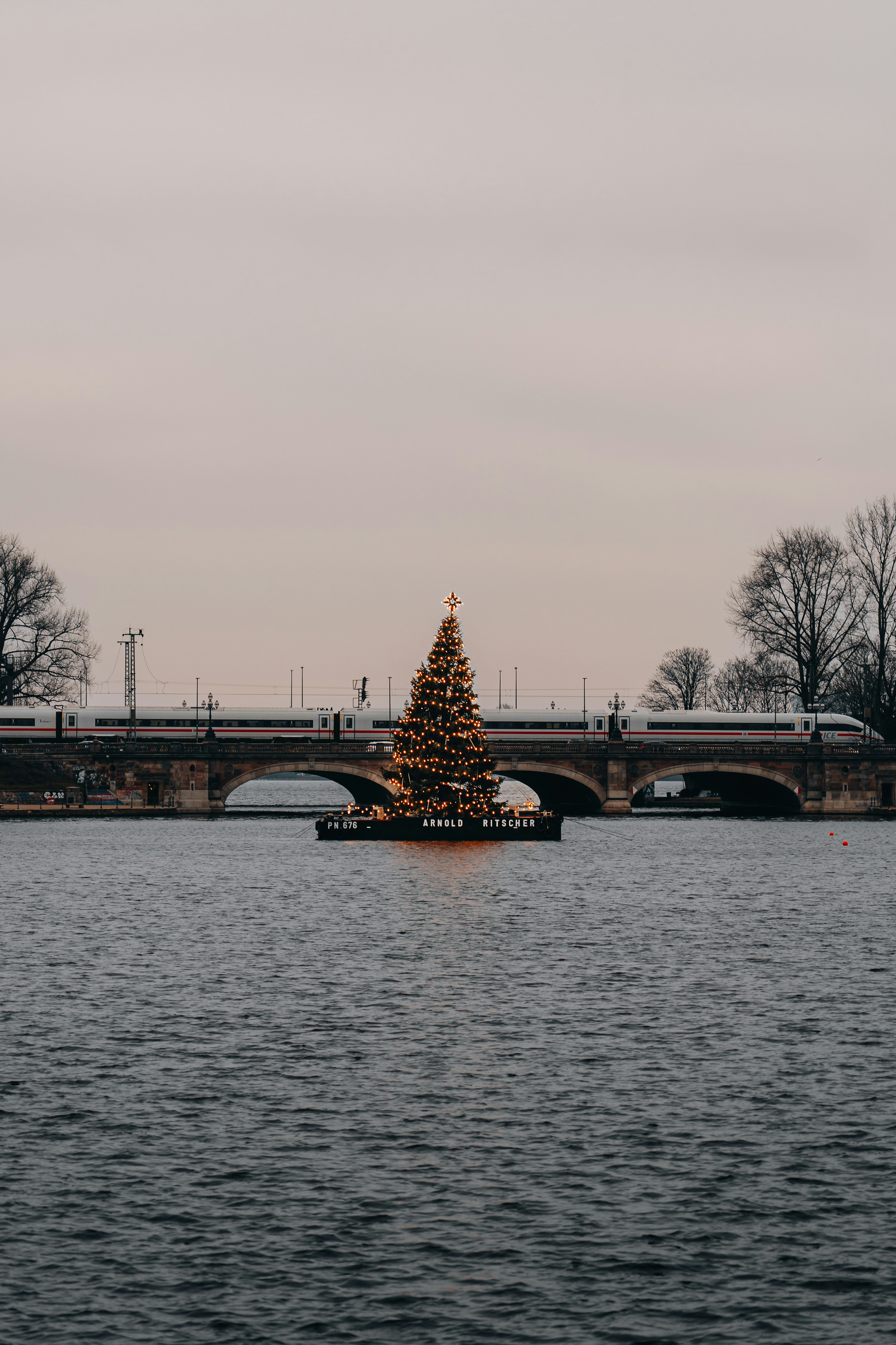 Midwinter Riverfloat: A Christmas Tree Barge Anchored Under the Arched Bridge