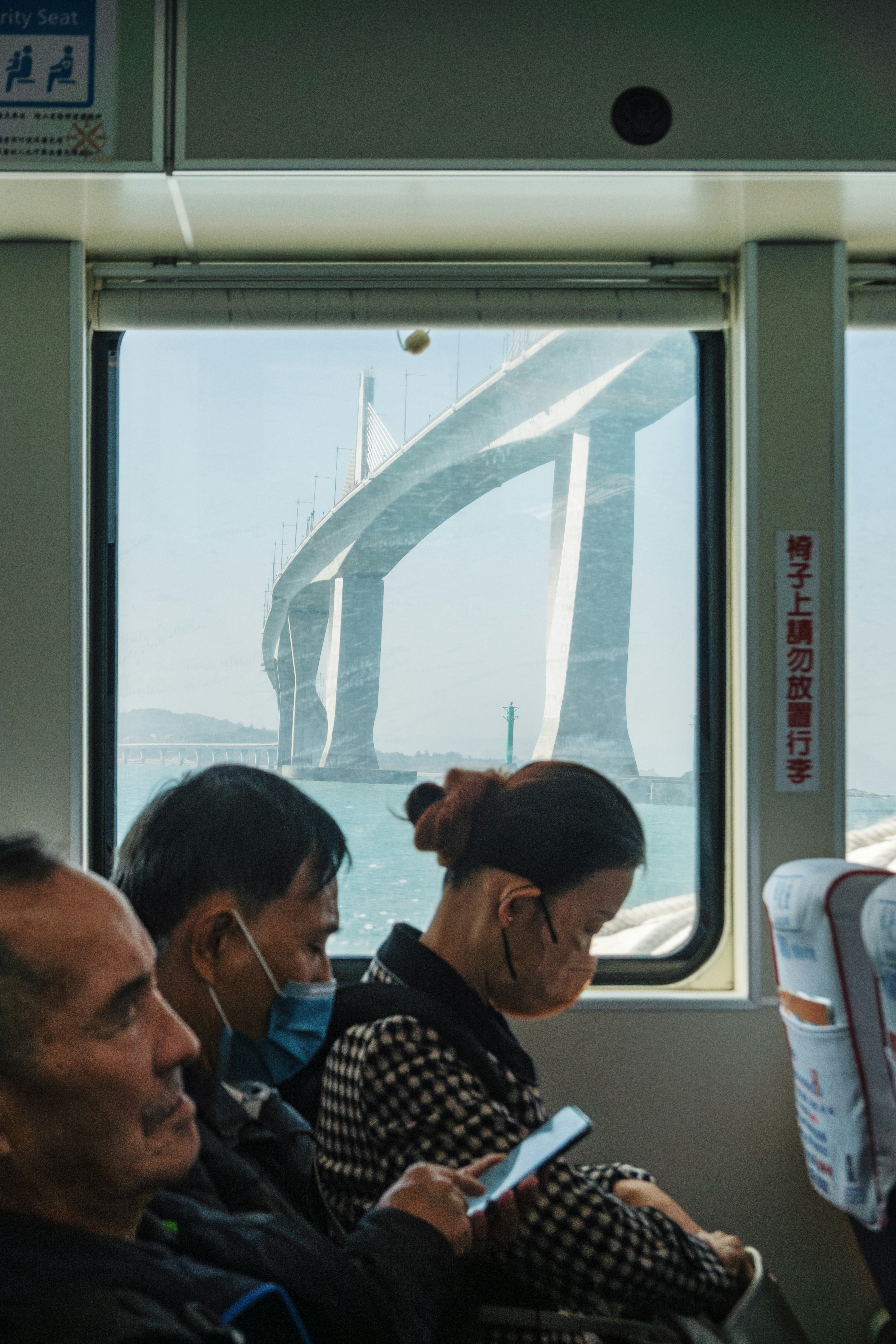 Crossing the View: Passengers in Quiet Focus Beneath a Bridge
