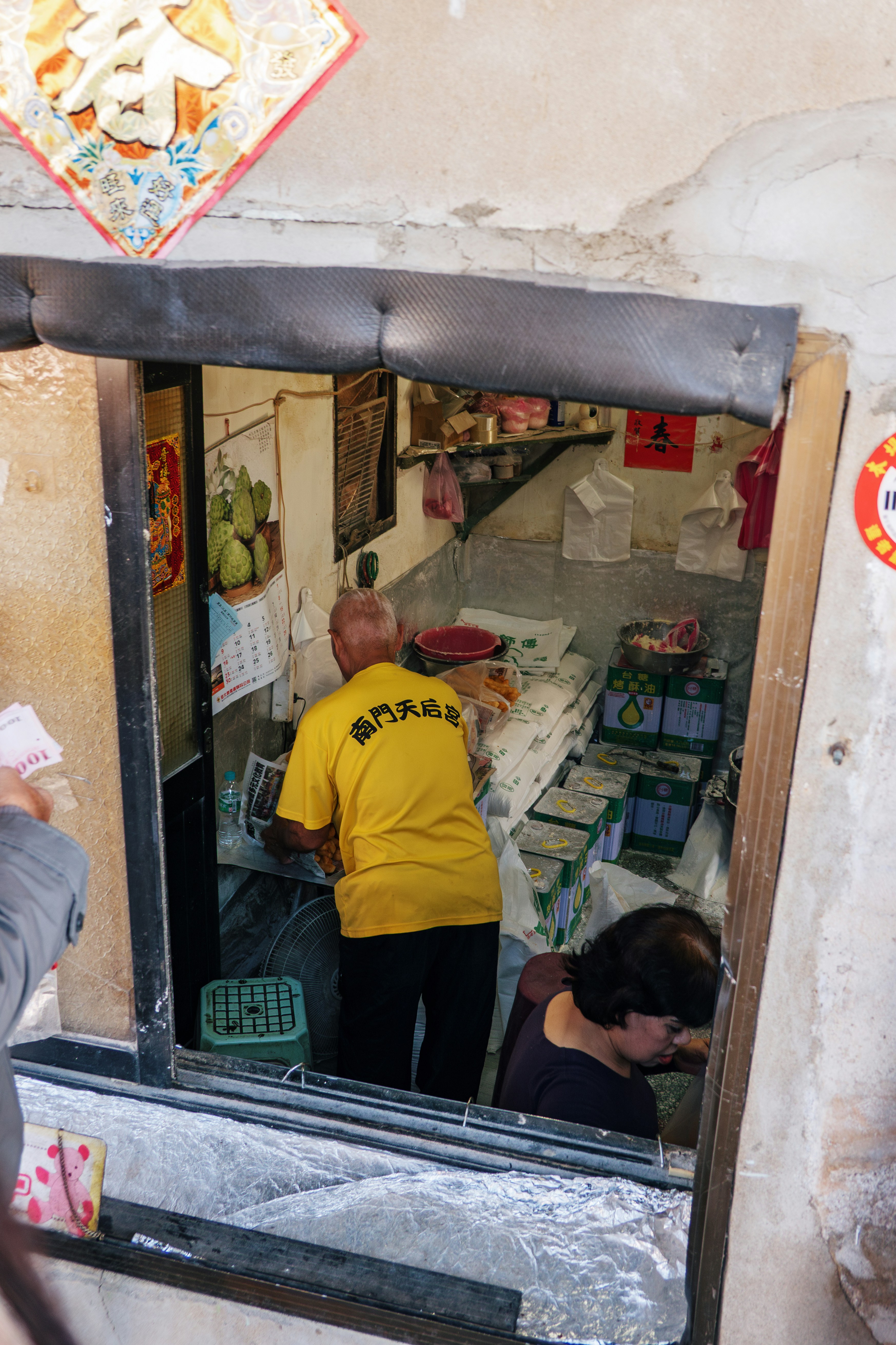 Yellow-shirted vendor amid a cluttered shop window with stacked goods
