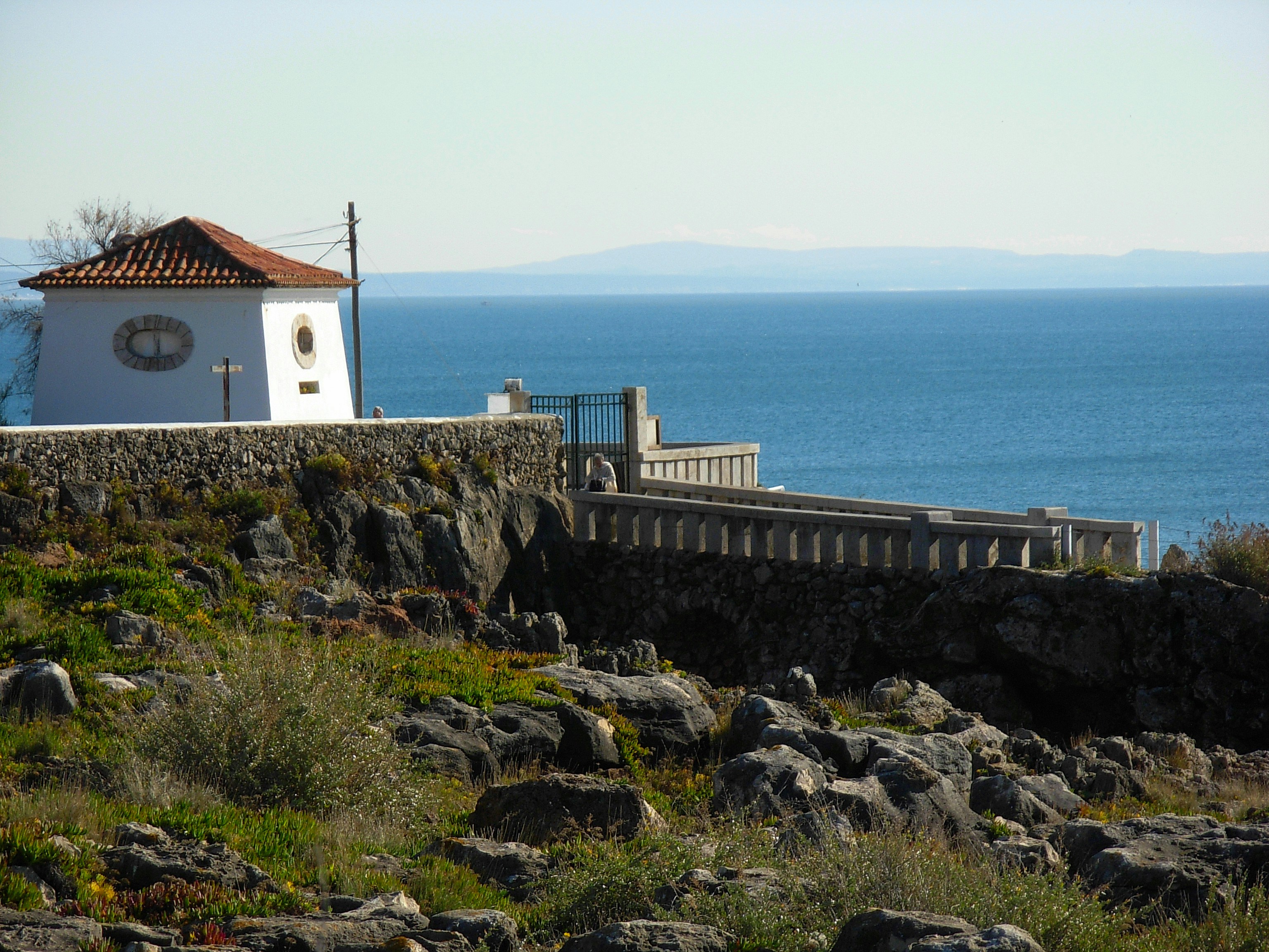 White building on rocky coast overlooking blue ocean