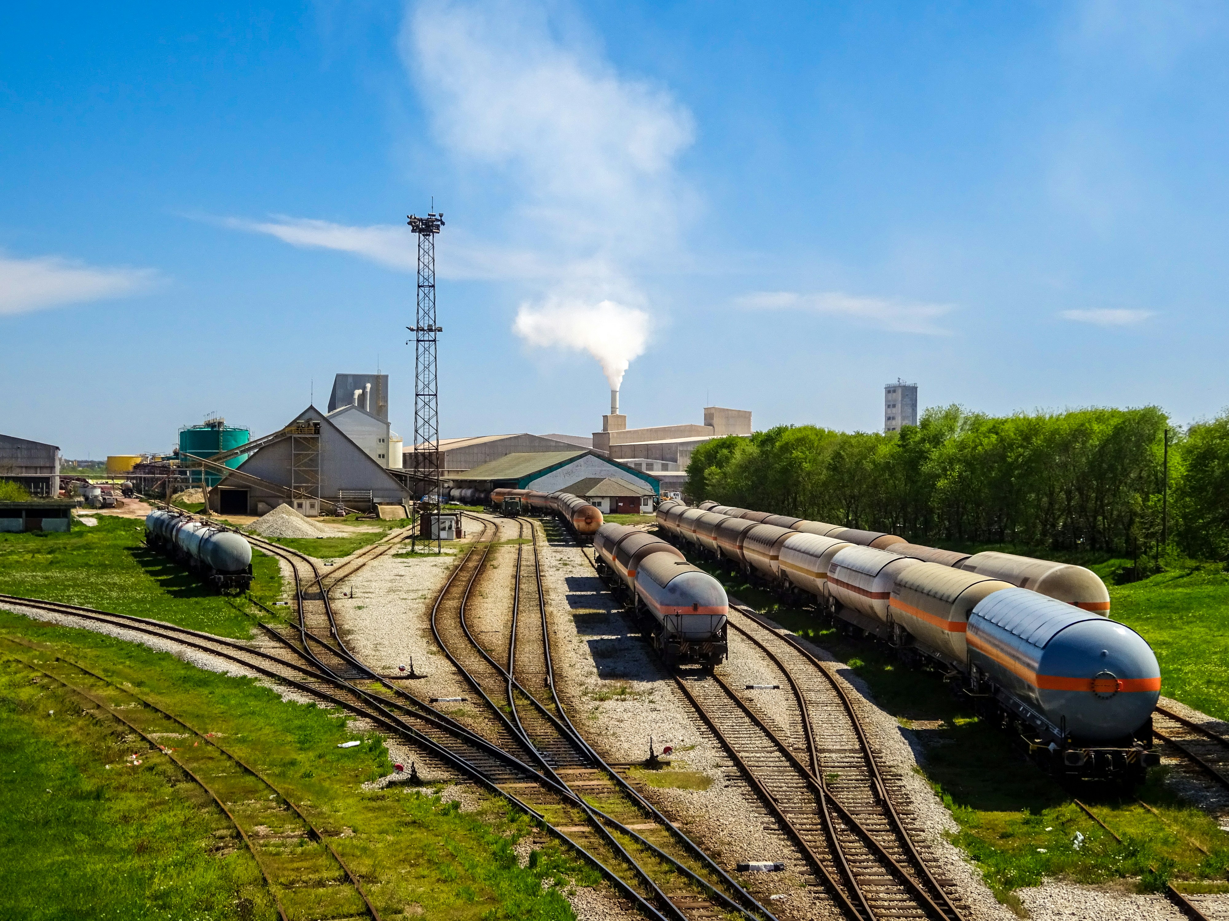 Trains at an industrial facility with smoke stacks.