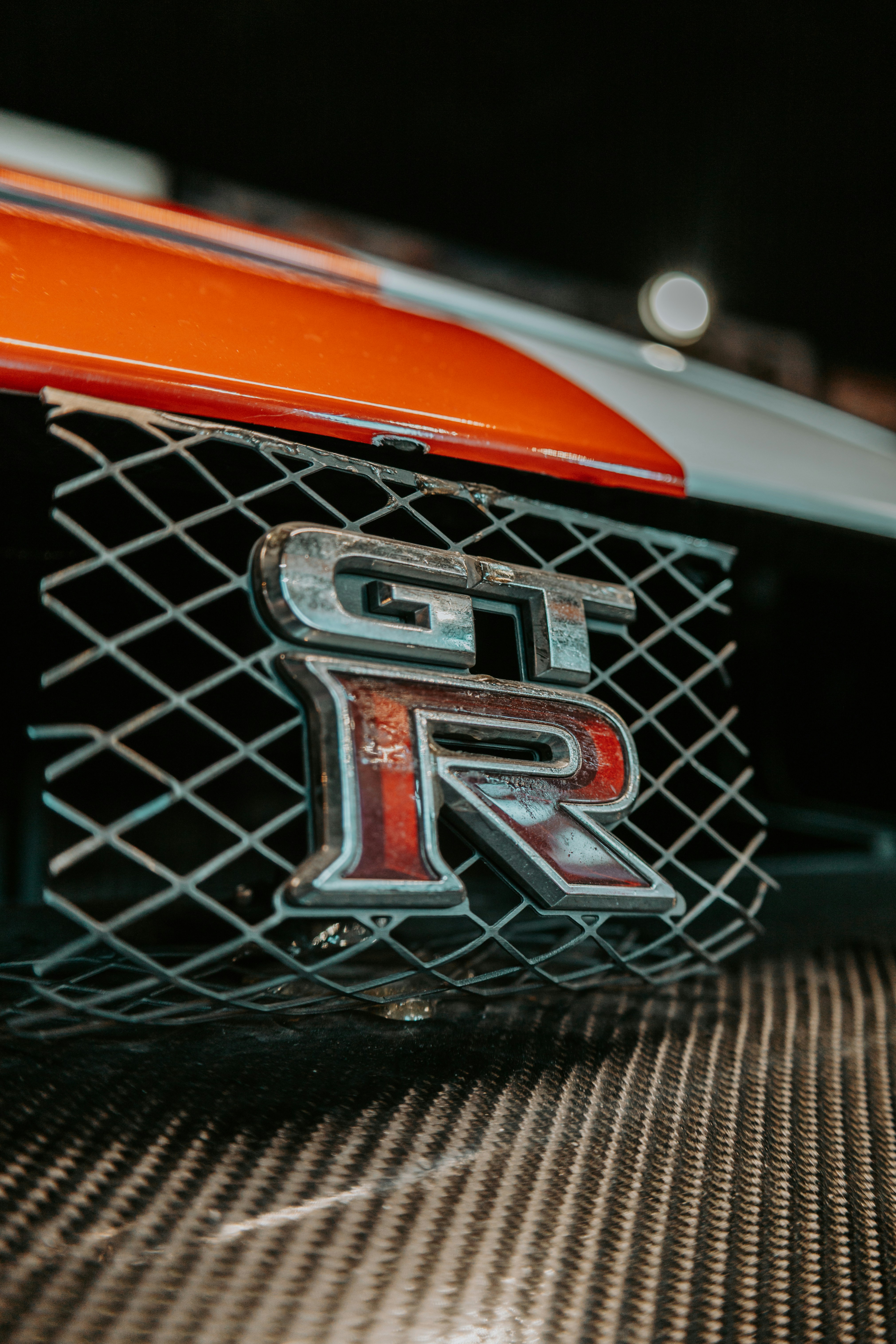 Close-up of a Nissan GT-R badge on a mesh grille with orange hood edge